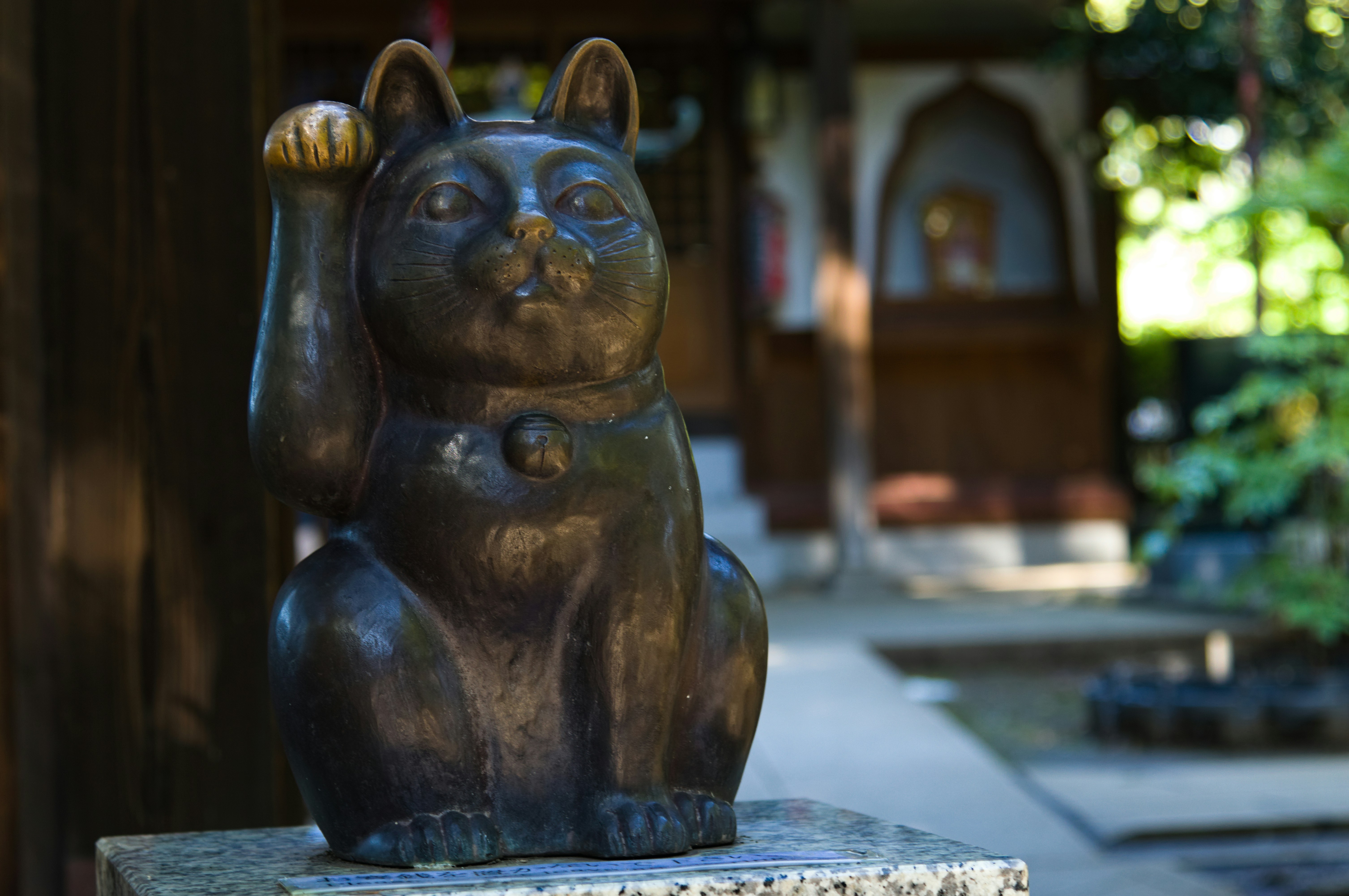 Raised Paw Guardian: A Shiny Cat Statue in a Quiet Shrine