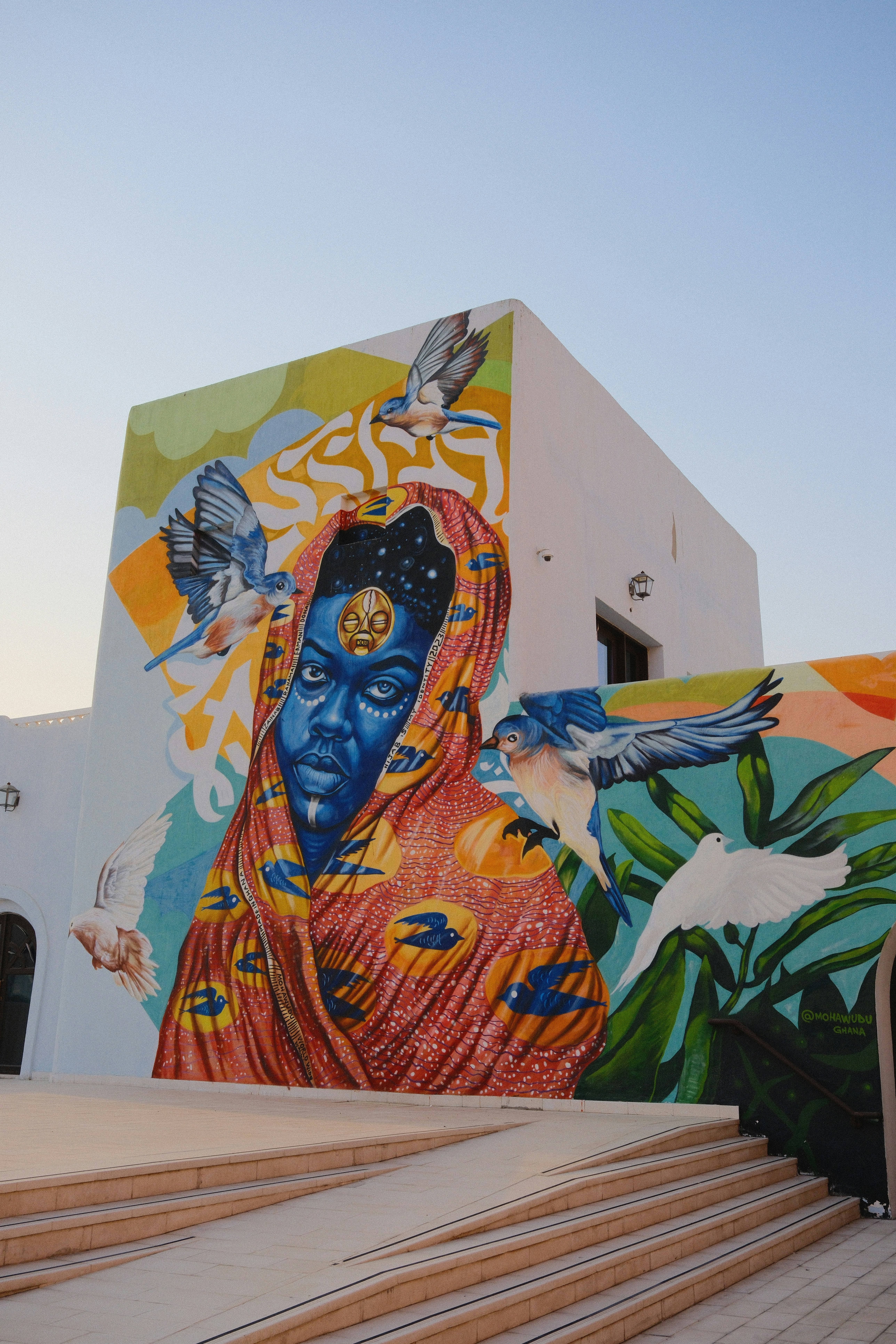 Vibrant mural of a veiled blue-eyed figure surrounded by soaring doves