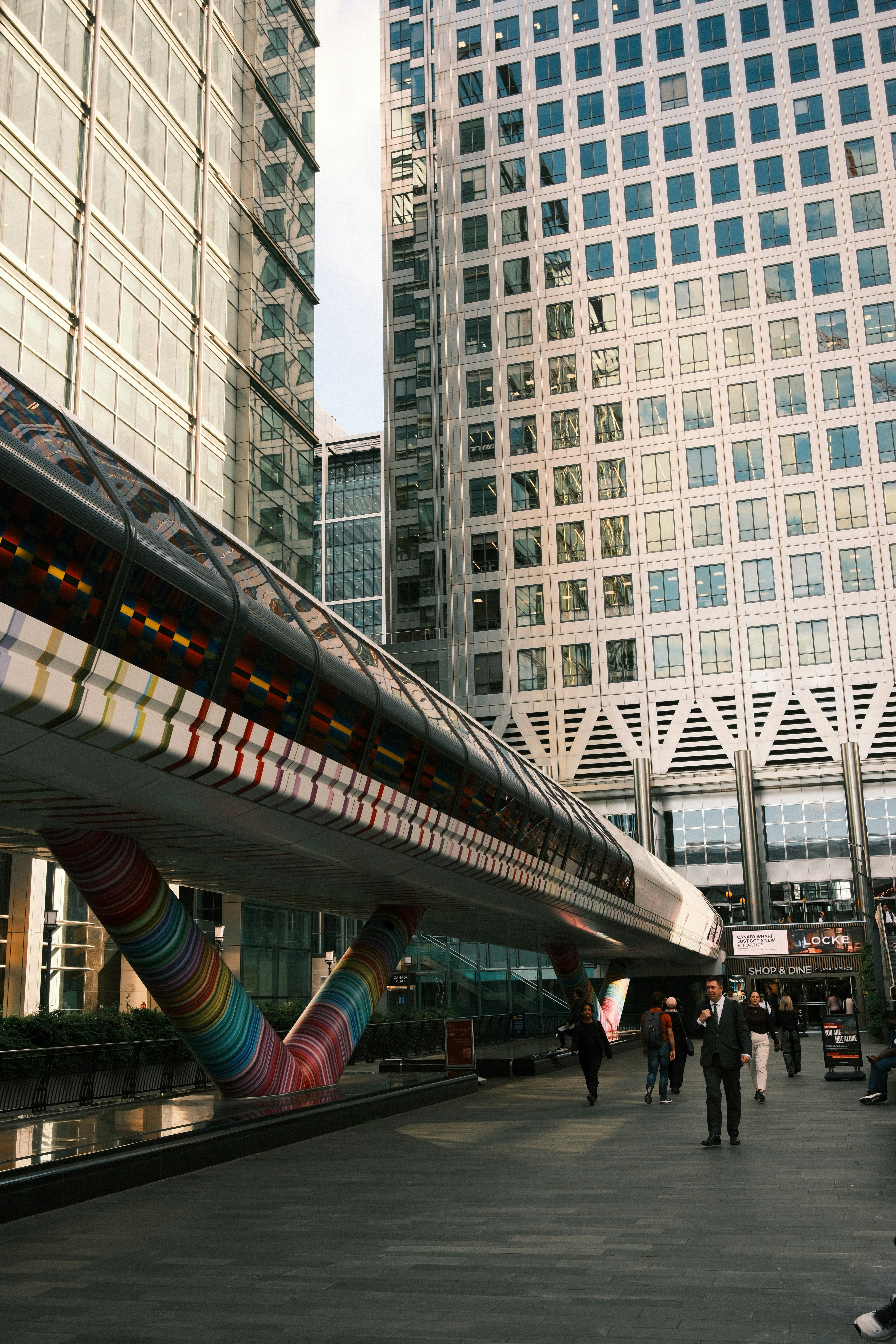Rainbow Columns under a Glass Sky: People Crossing a Modern Atrium