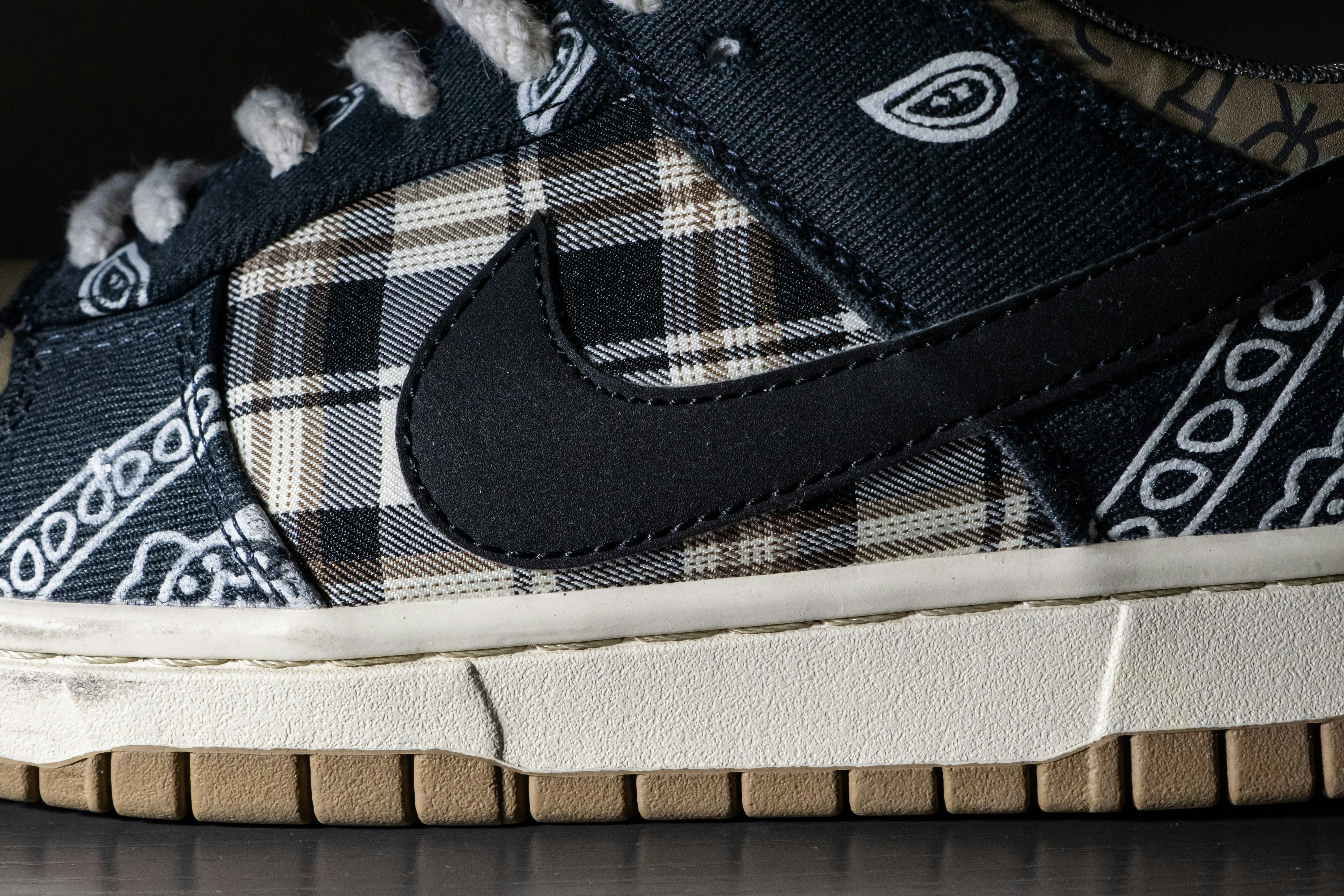 Close-up of a plaid-patterned Nike sneaker sole with prominent Swoosh, emphasizing texture and stitching details; appears as a product or lifestyle shot, focusing on material and contrast.