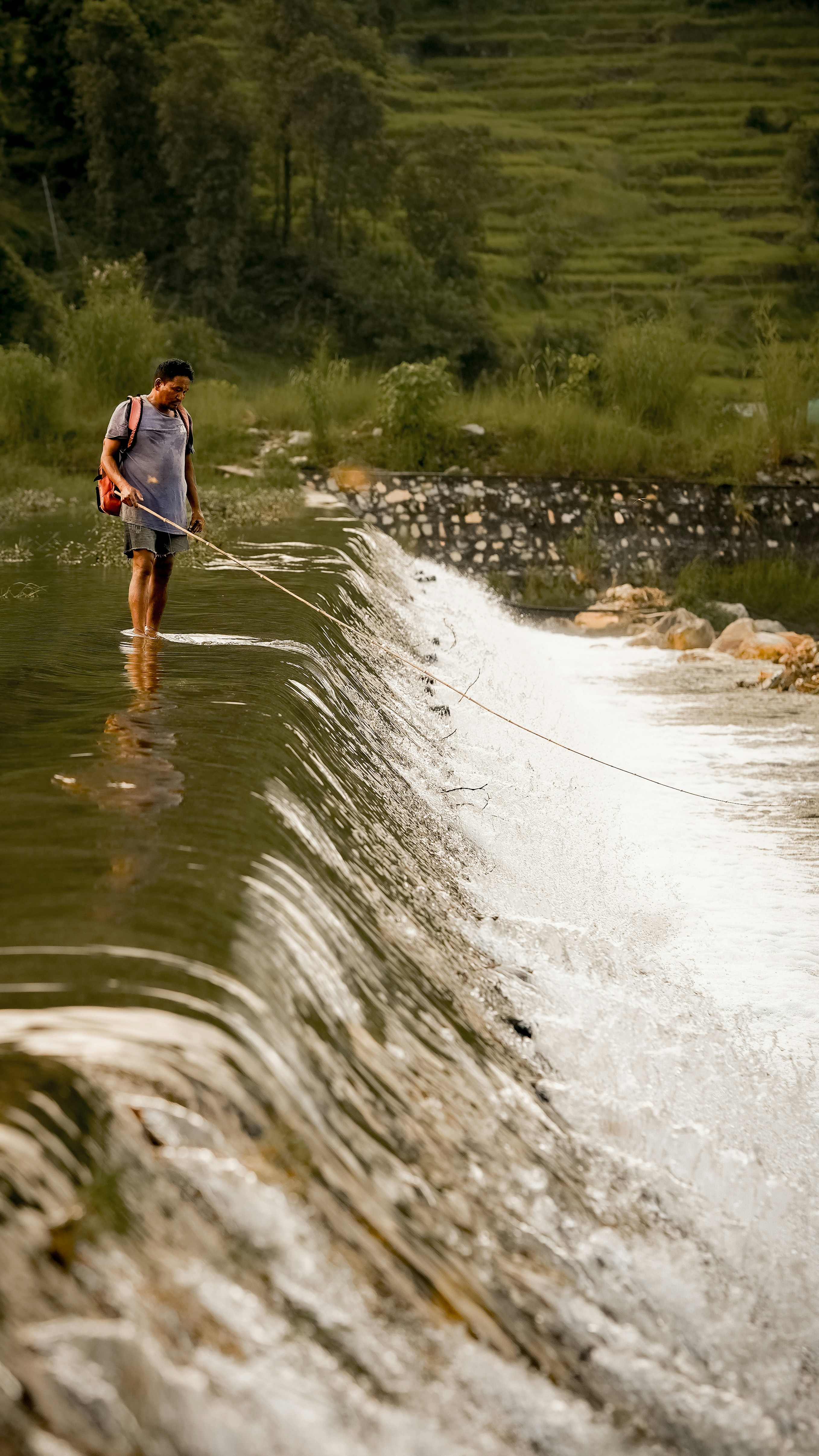 A lone fisherman balances at the edge of a rushing spillway