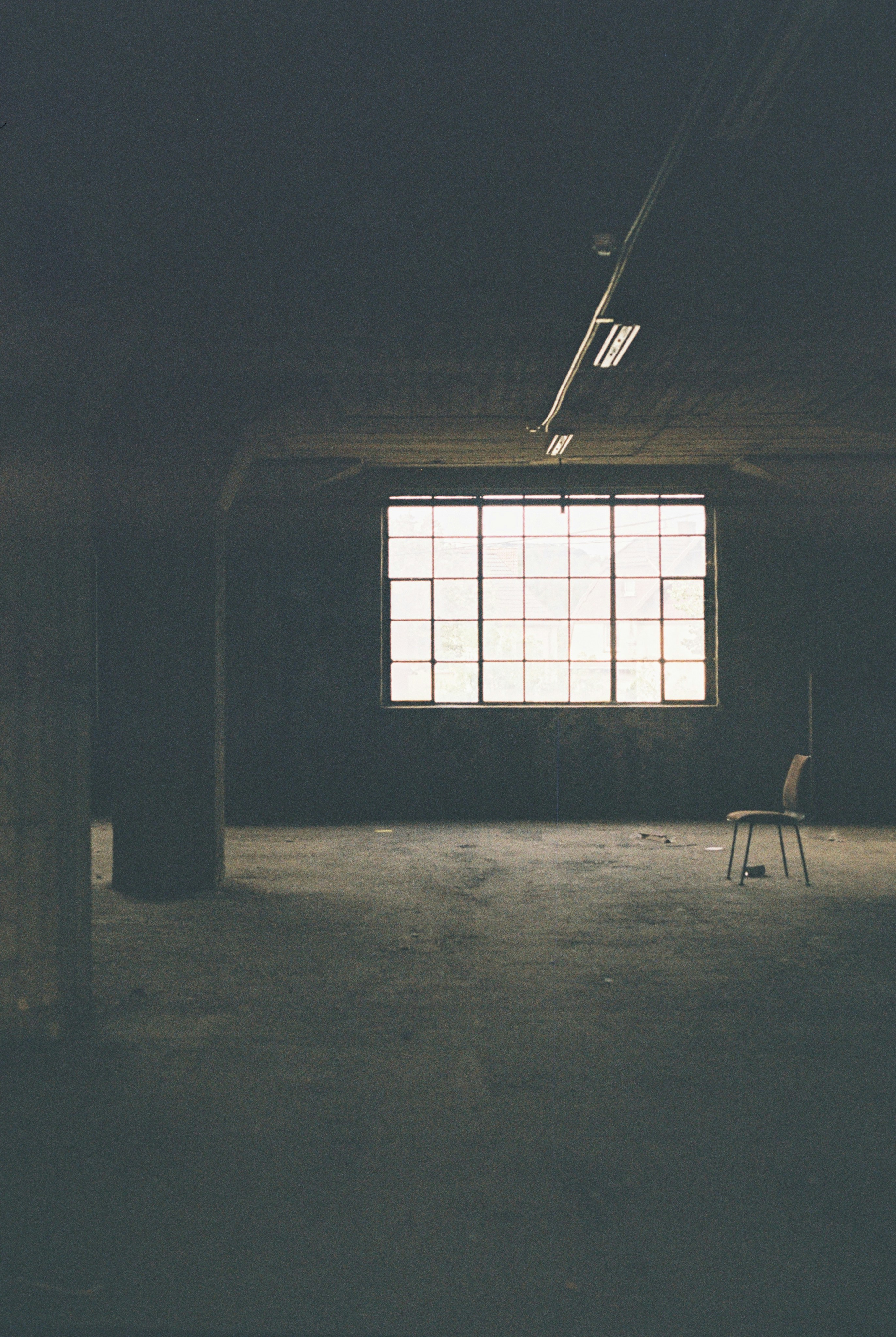 A single chair in a dark, empty industrial room with a large window