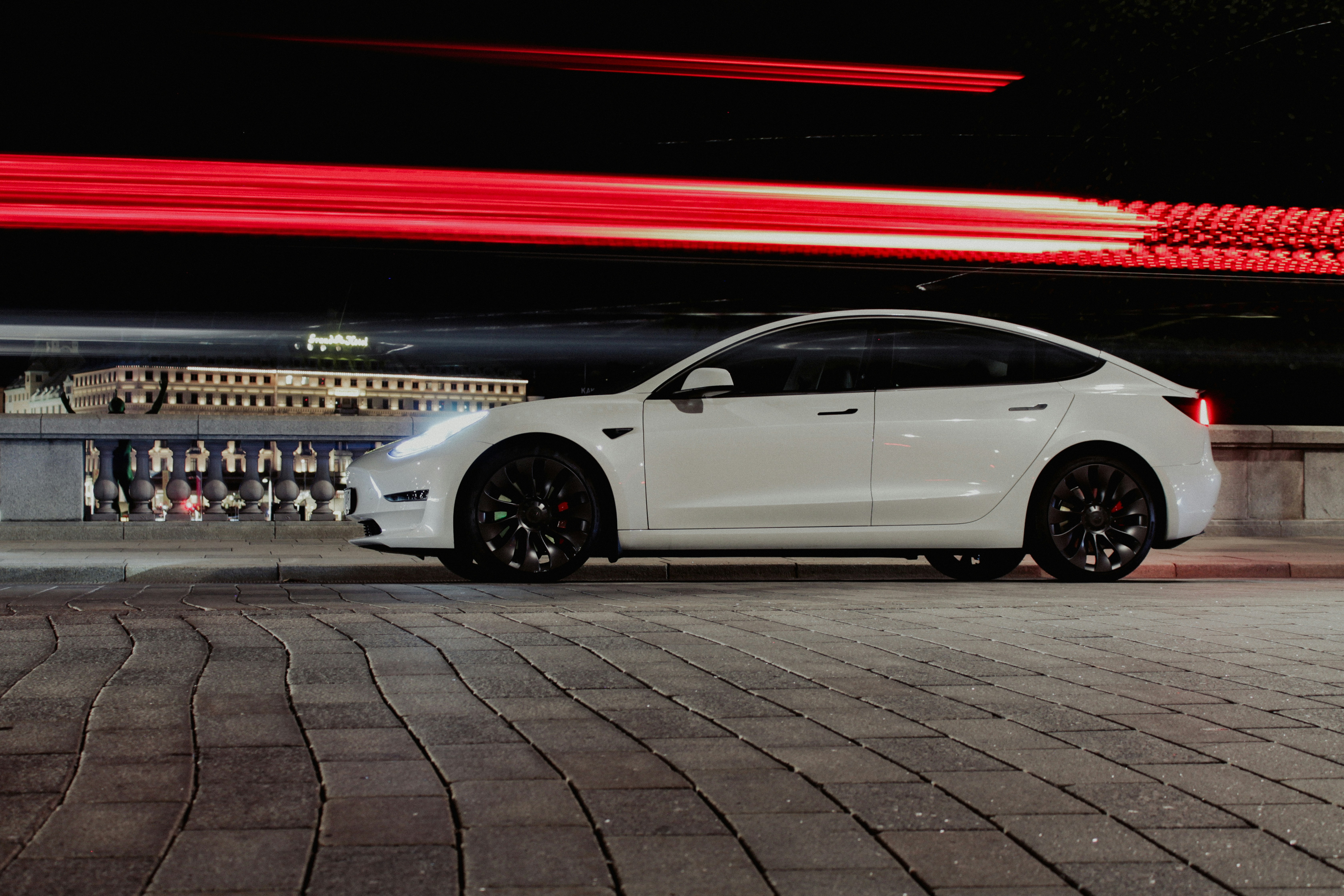 White Tesla-like Coupe in Motion Blur Streaks Across a City Square