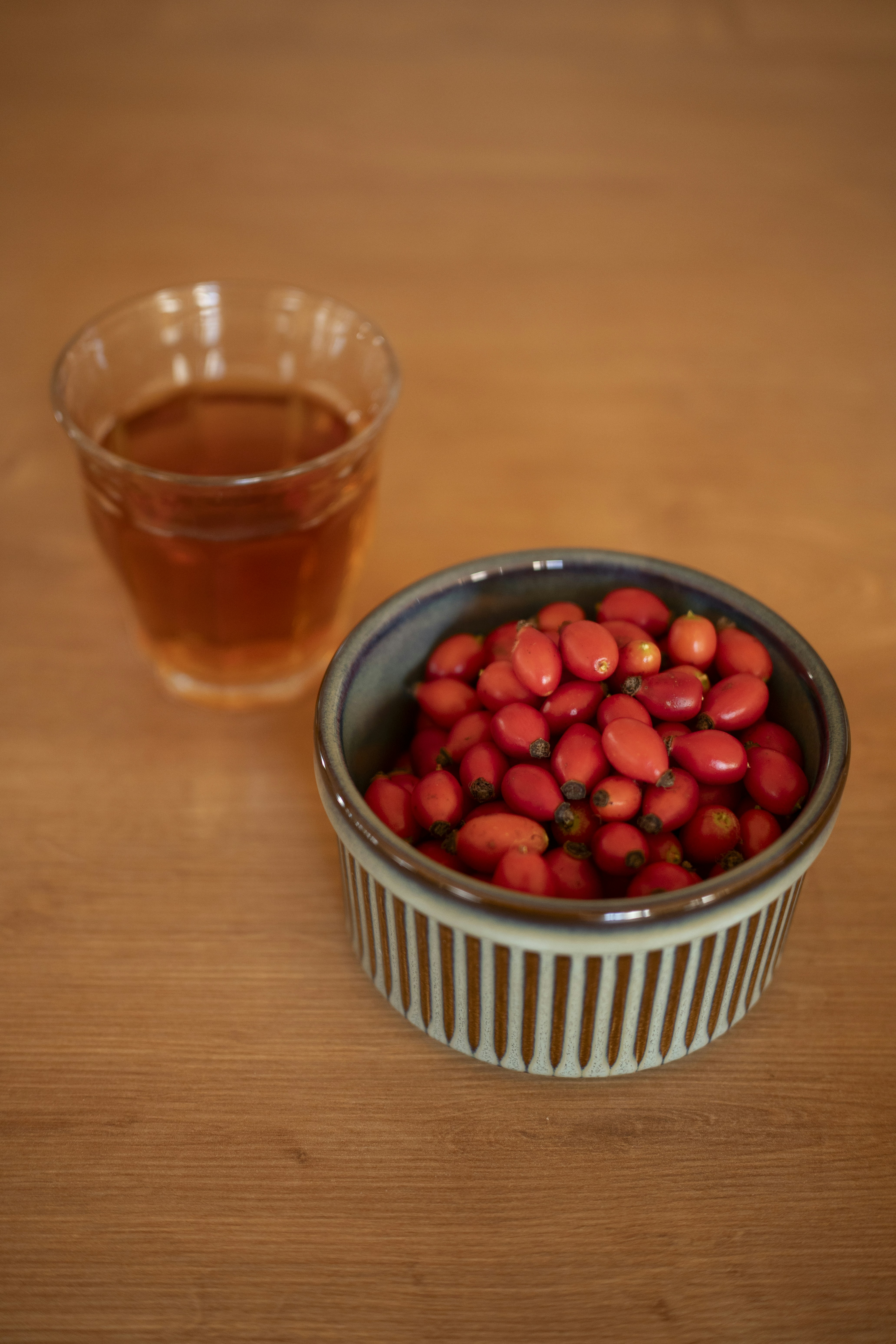 Crimson Berries in a Ceramic Bowl with a Glass on a Warm-wood Table