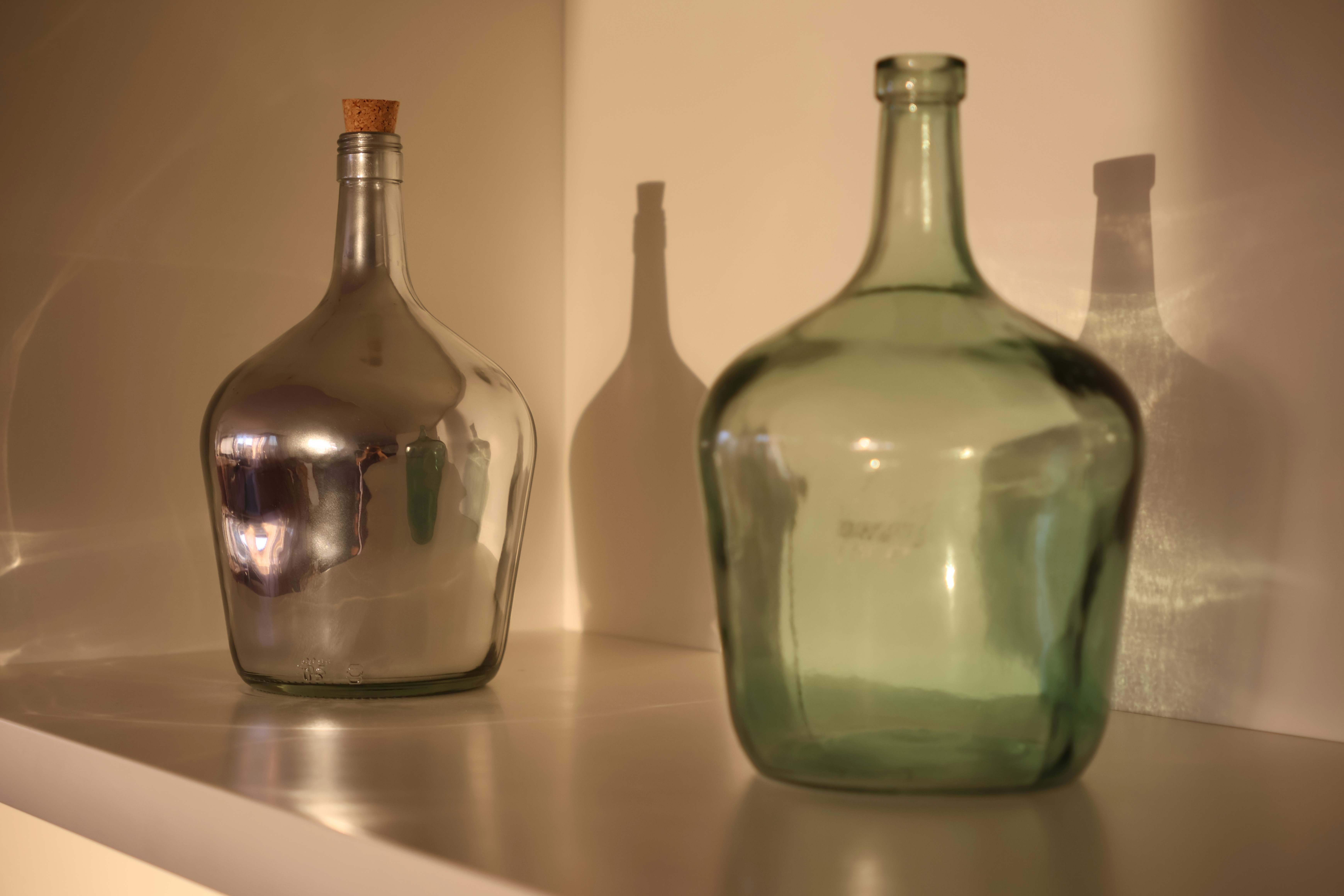 Two vintage glass bottles sit on a softly lit shelf, their shapes and muted colors creating a calm still-life.