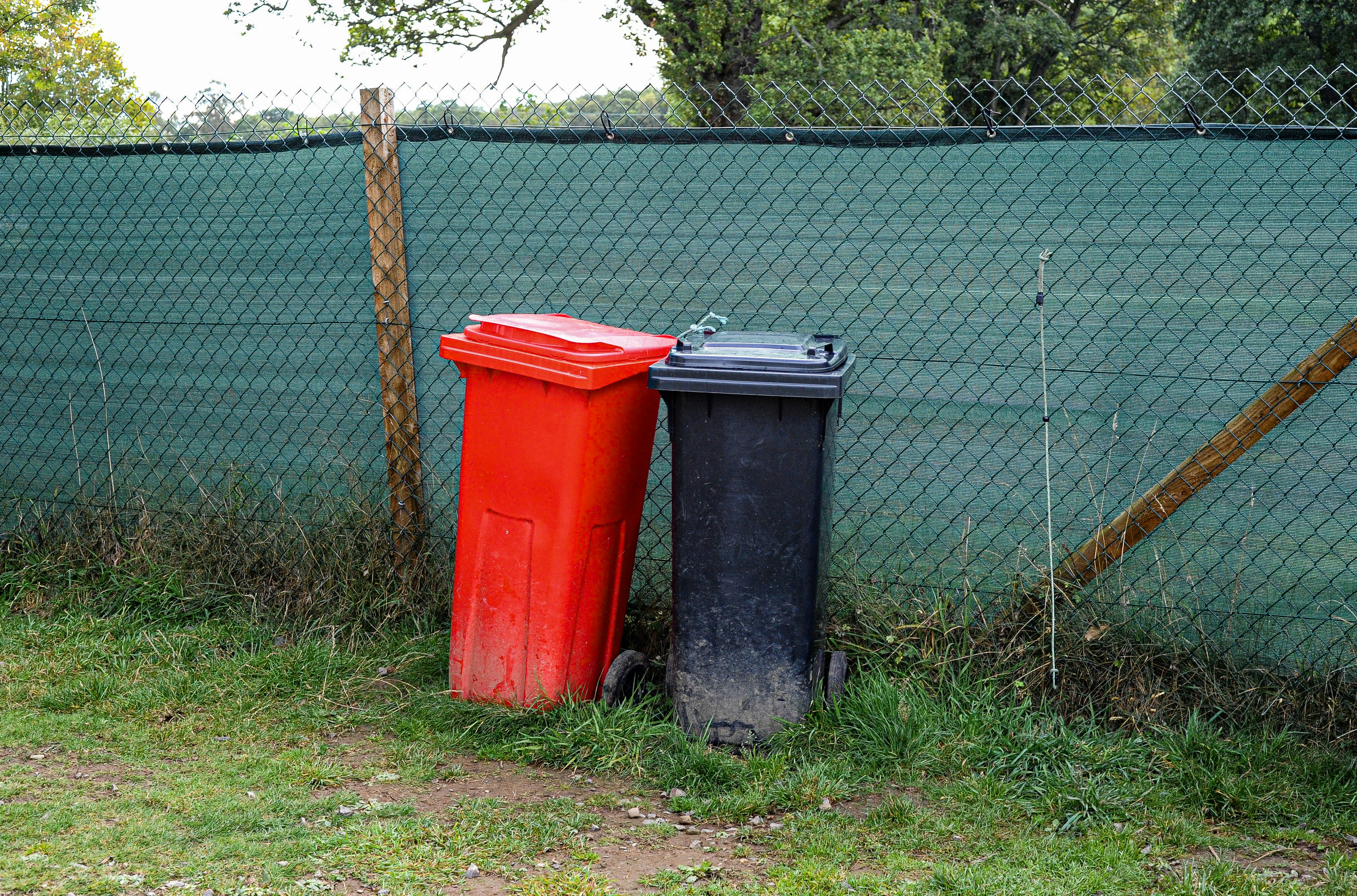 Two Trash Bins Stand Guard by a Woven Fence