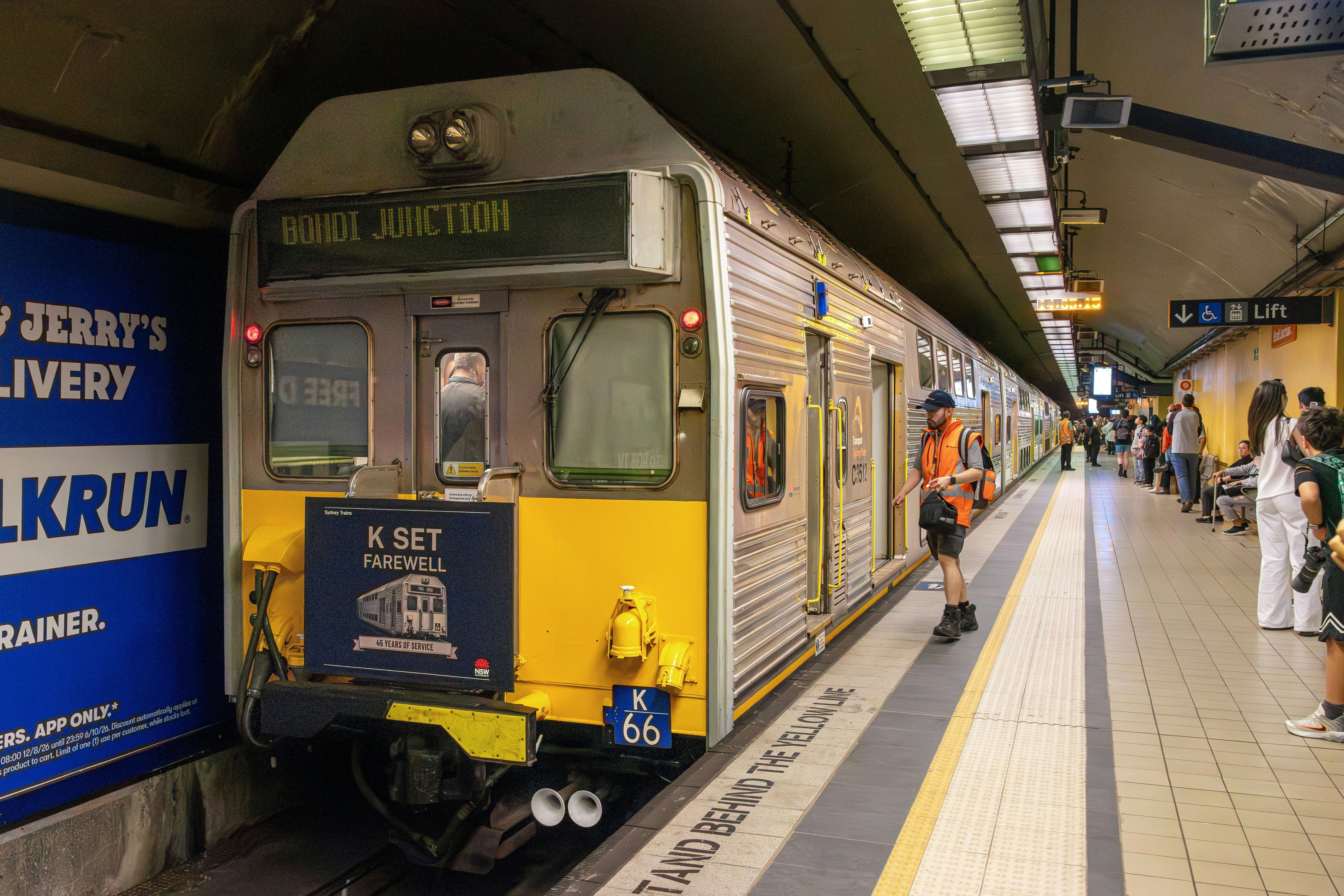 Commuters and a yellow subway train occupy a busy station platform, captured with the emphasis on the front car and approaching passengers.
