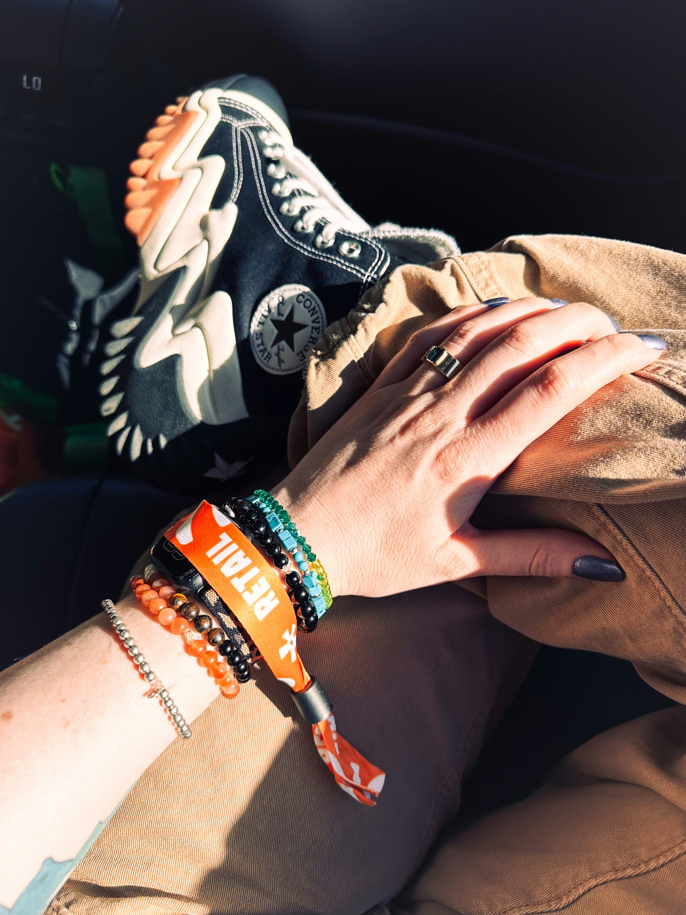 A person wearing beaded bracelets and a wristband resting a hand on tan trousers
