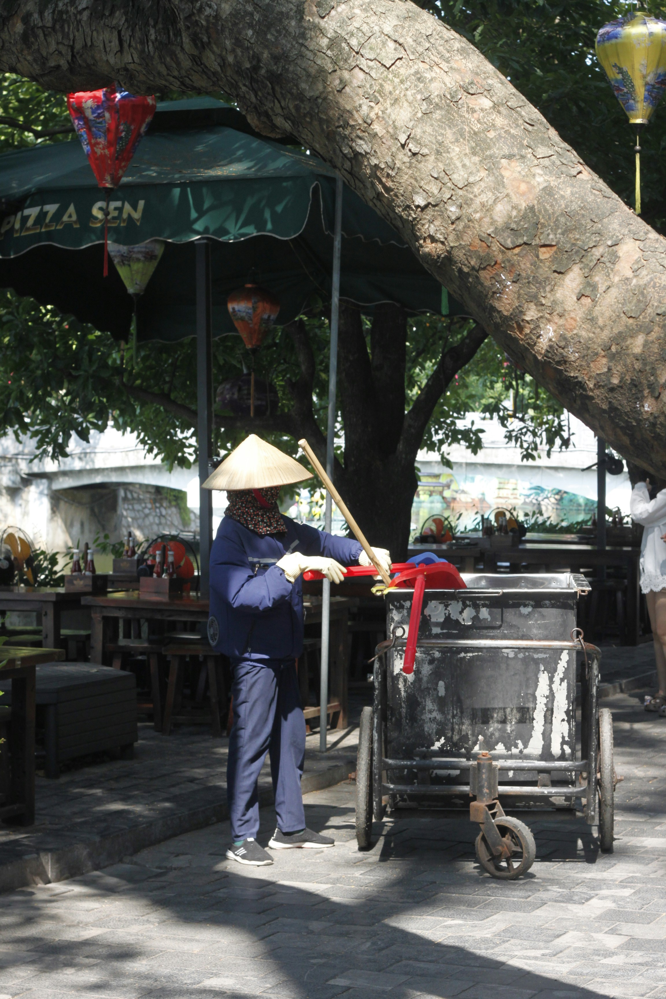 Slinging Rain-Ready Tomato Fans: A Street Vendor at Rest Under a Giant Branch