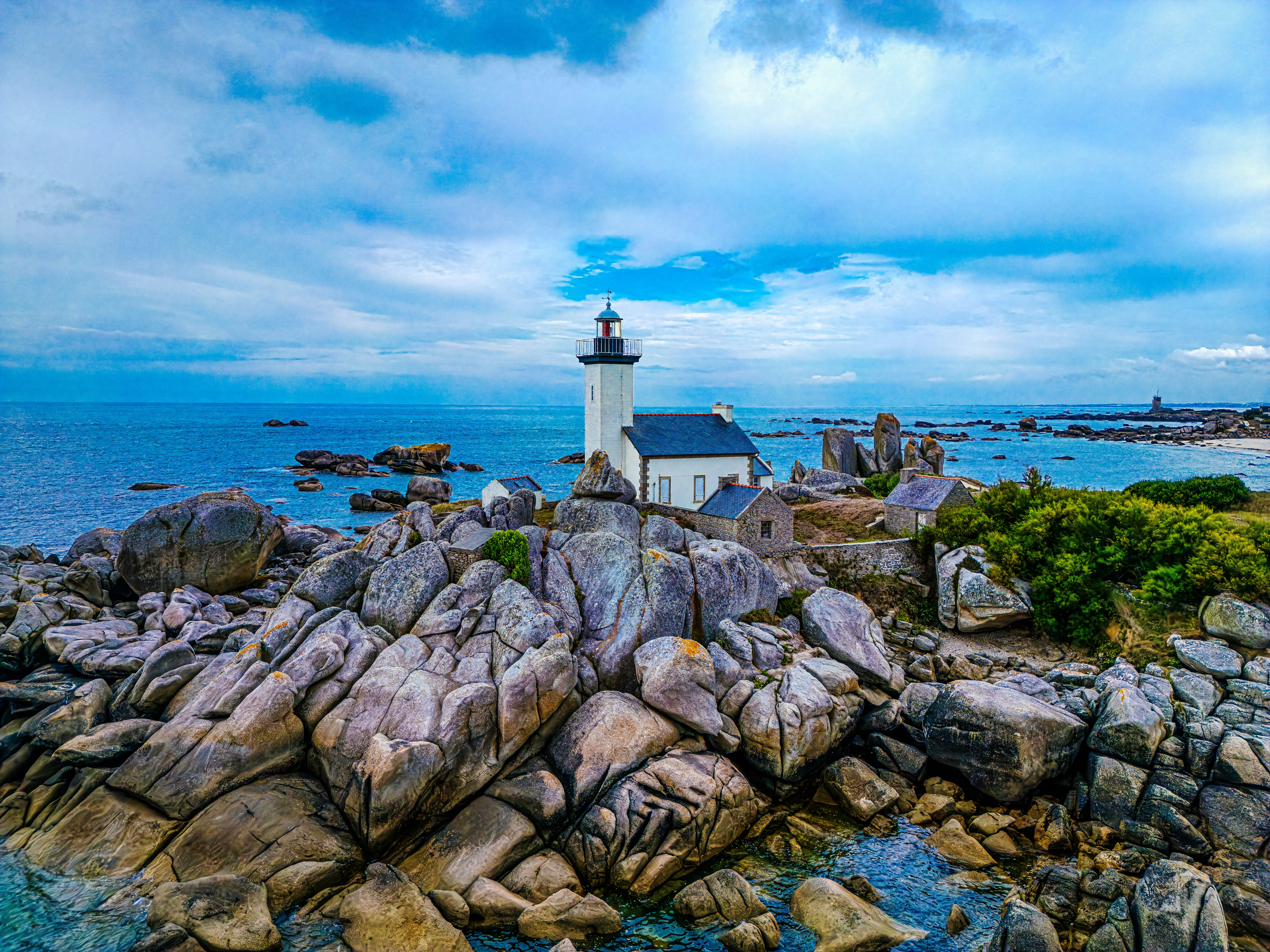 Coastal lighthouse perched amid rugged granite rocks with a calm sea beyond, a scene of coastal architecture and weathered stone.