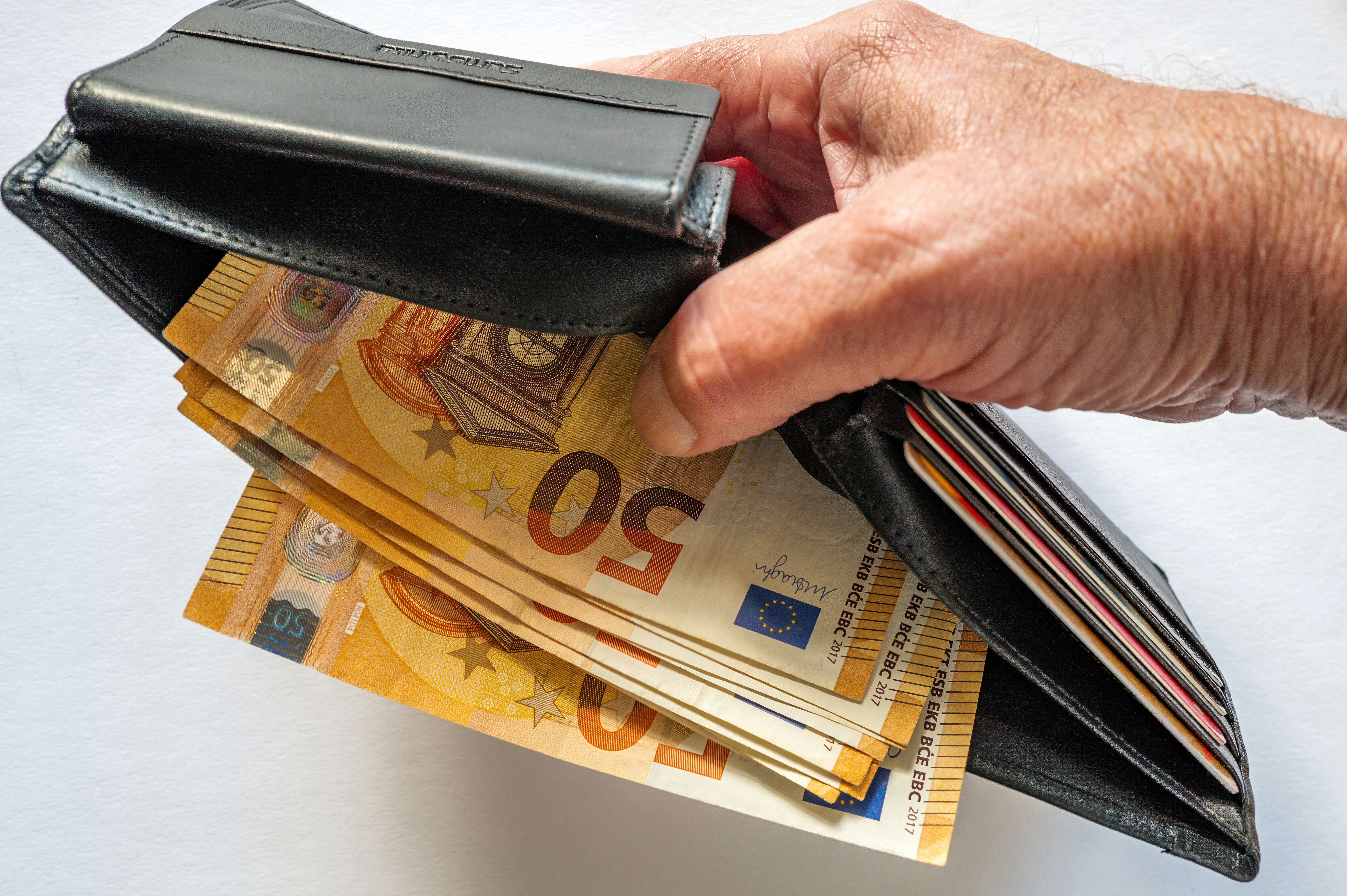 Close-up of a black leather wallet held open with several euro banknotes partially visible, emphasizing currency and everyday carrying accessories.