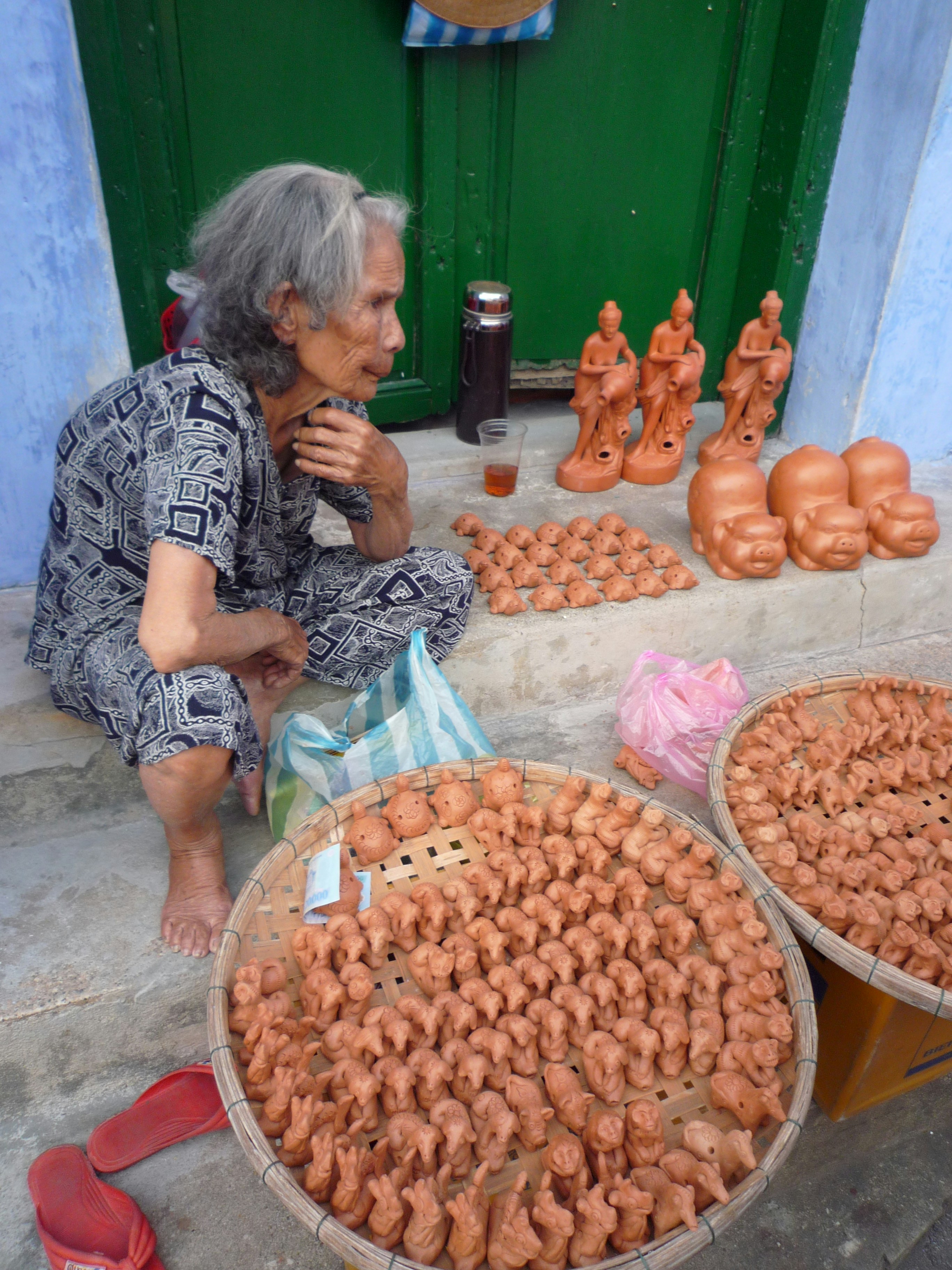 Verdant doorway and clay figures: an elder vendor amid a trove of terracotta sculptures