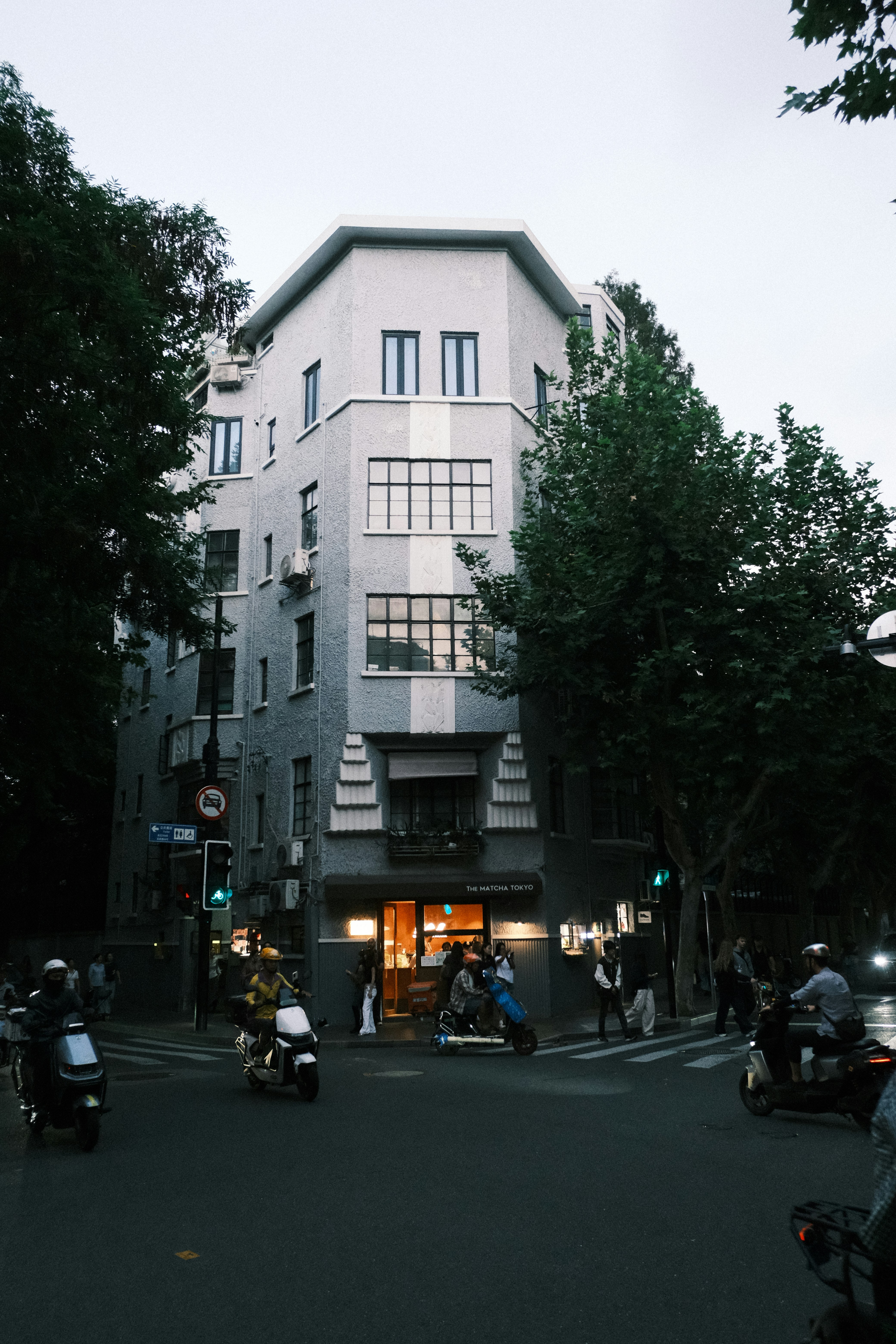 Urban dusk: street-level scene at a sunlit shopfront framed by a corner building