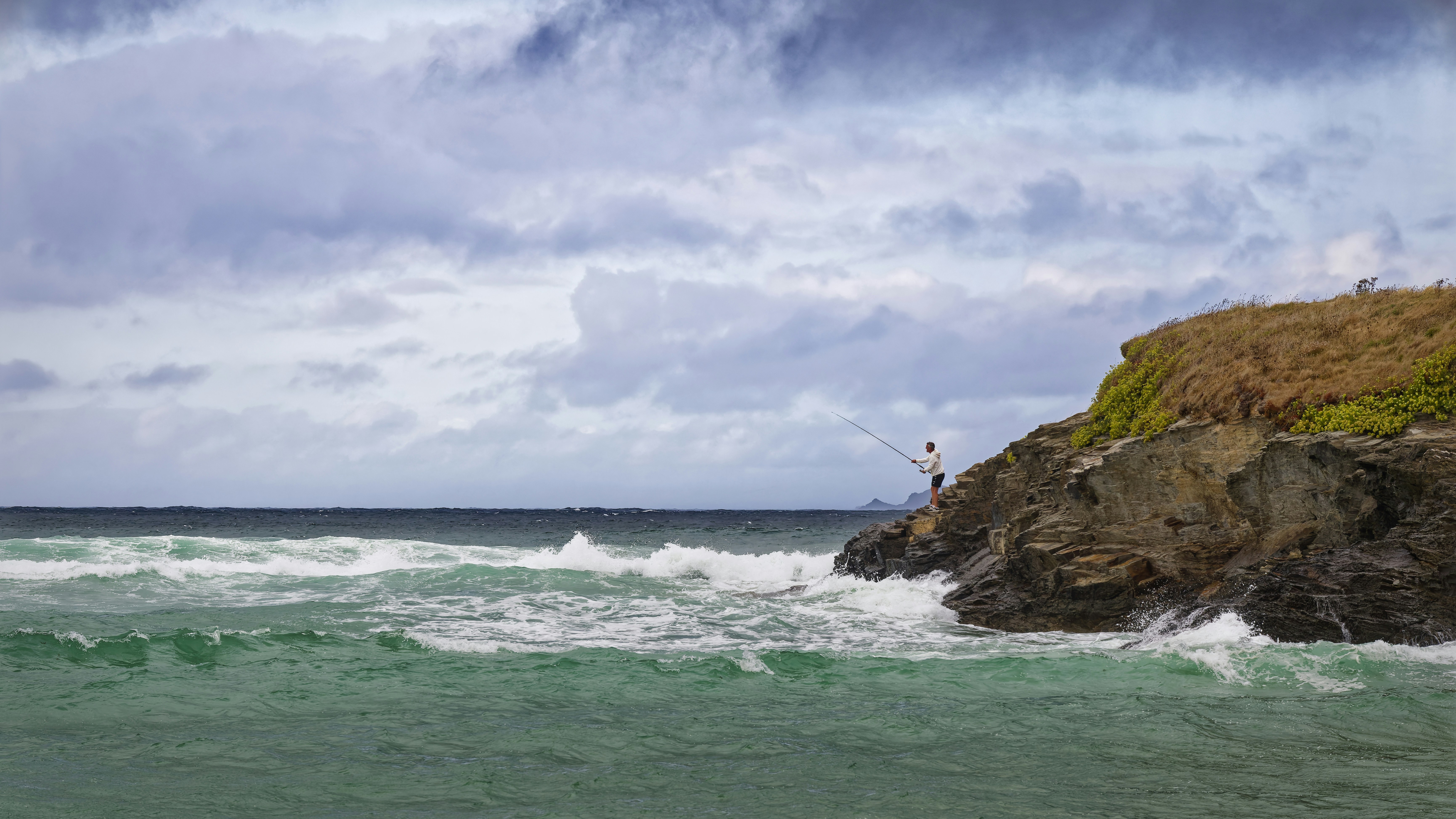 Cliffside Break: A Lone Angler at the Edge of Turquoise Waves