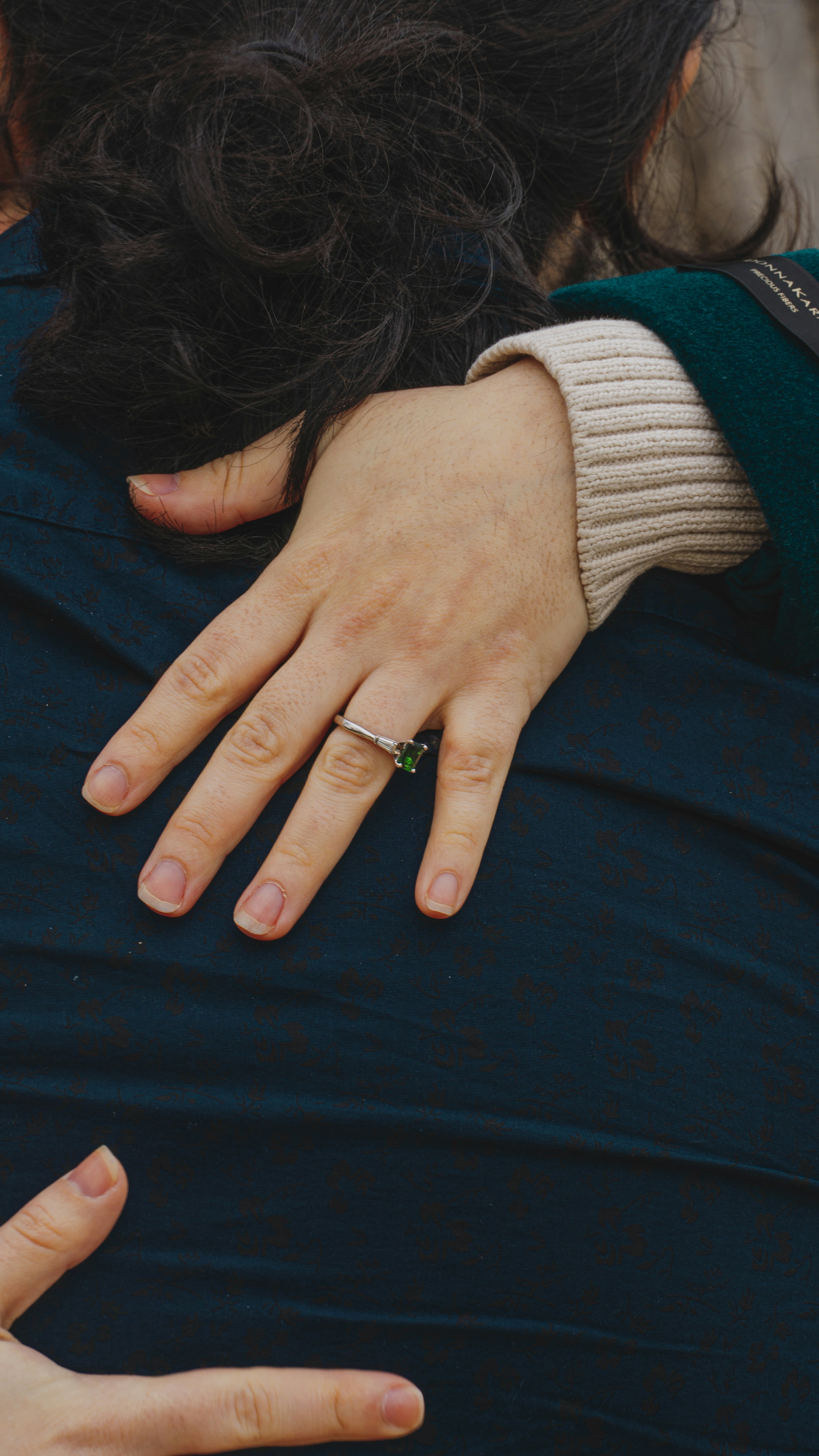 Shared moment: a hand with a ring rests on a shoulder in a quiet embrace