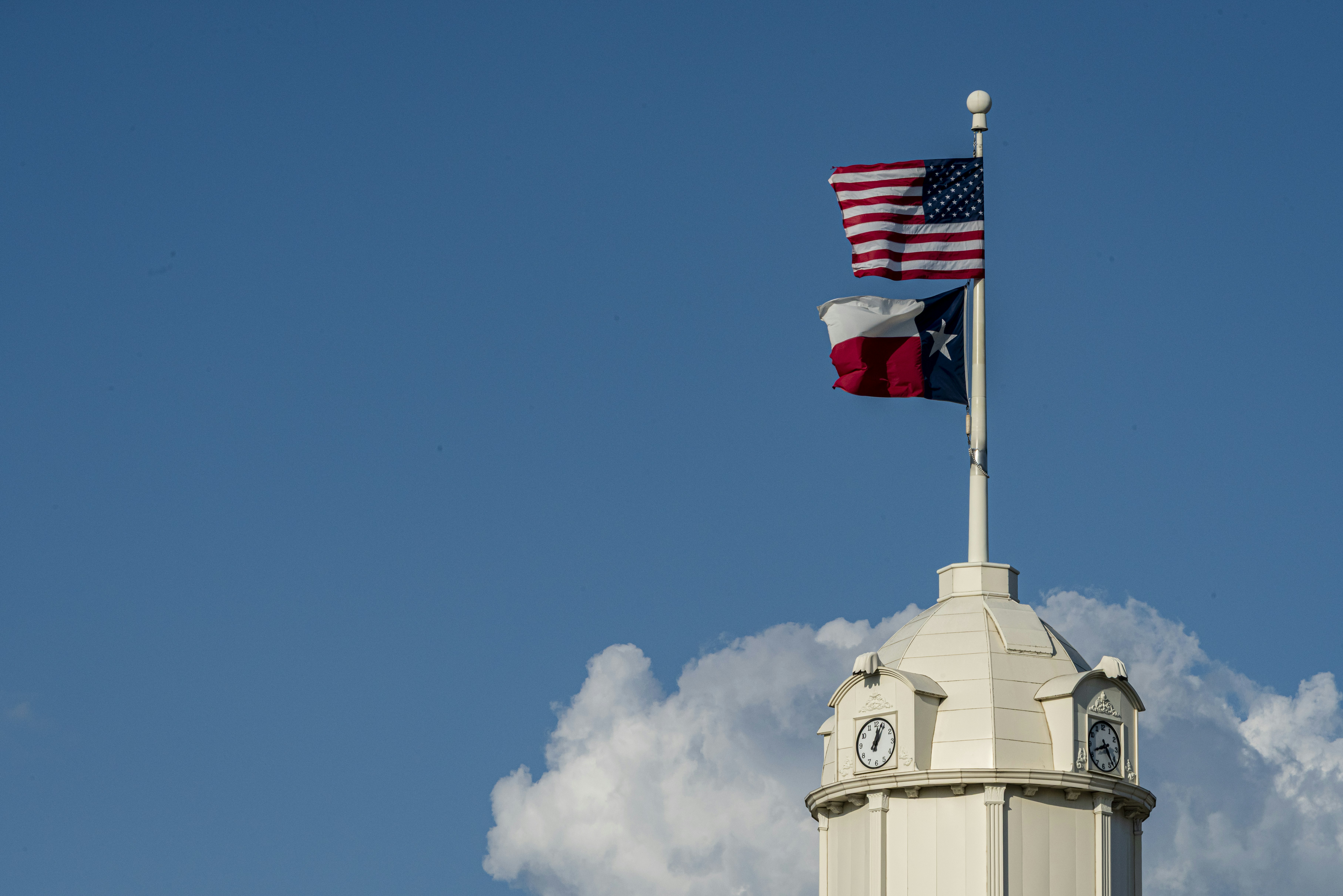 The dome along with the American and Texas State flags of the Hamilton county courthouse, in Texas, with a large white cloud looming behind the dome.