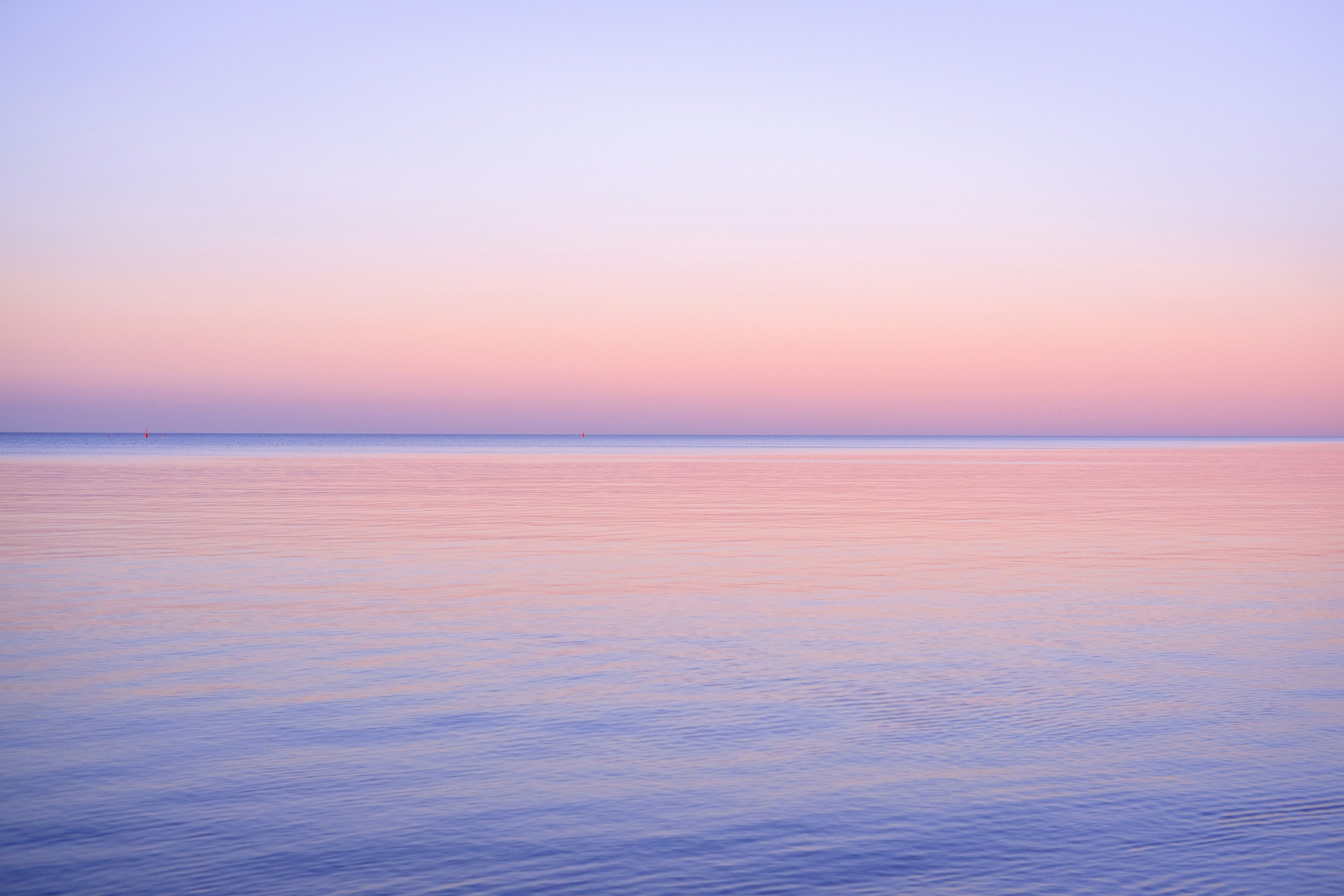 Calm water reflecting a soft gradient of pink and purple light at low sun