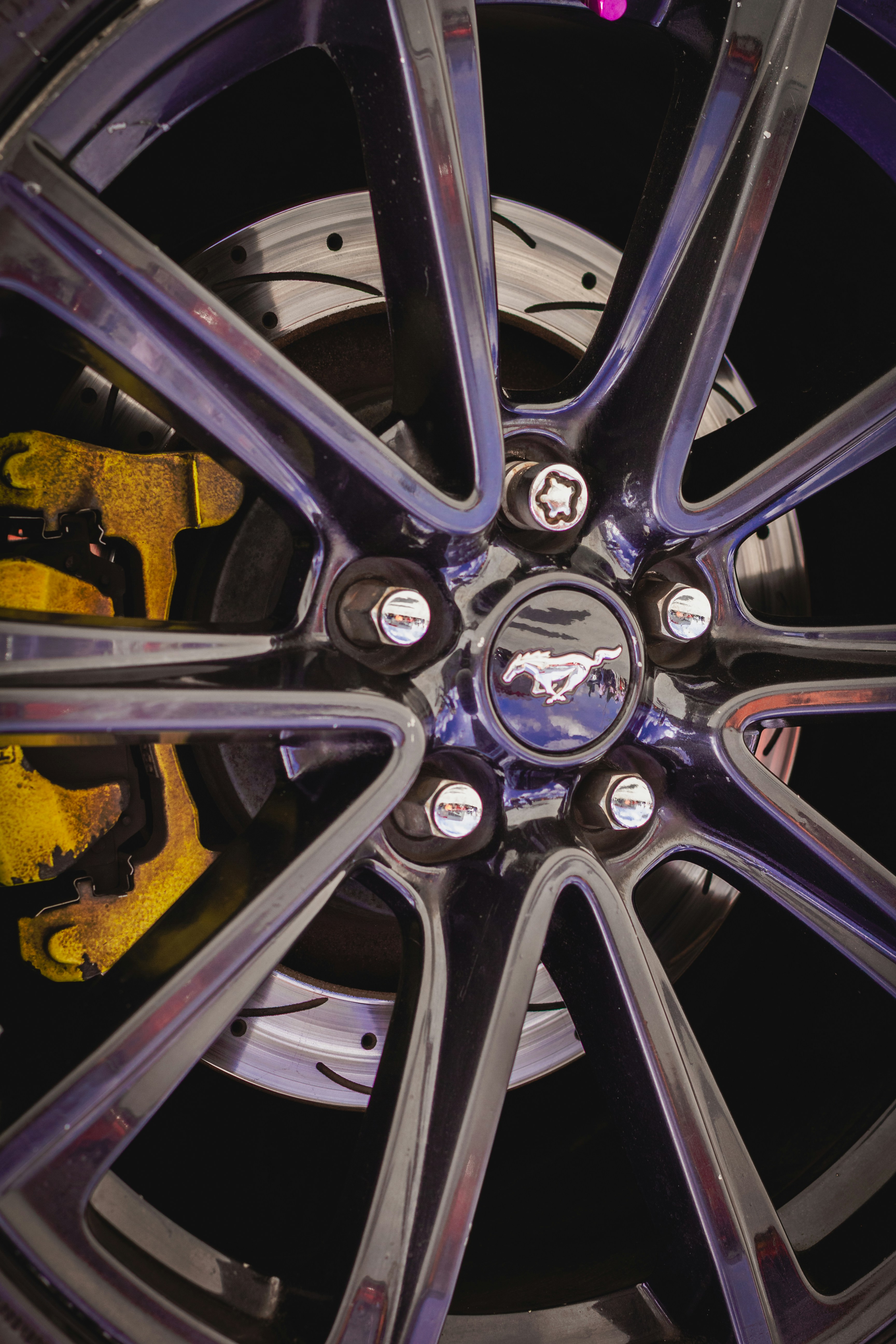Close-up of a car wheel with the Mustang emblem at center, showing spokes, brake caliper, and rotor details.
