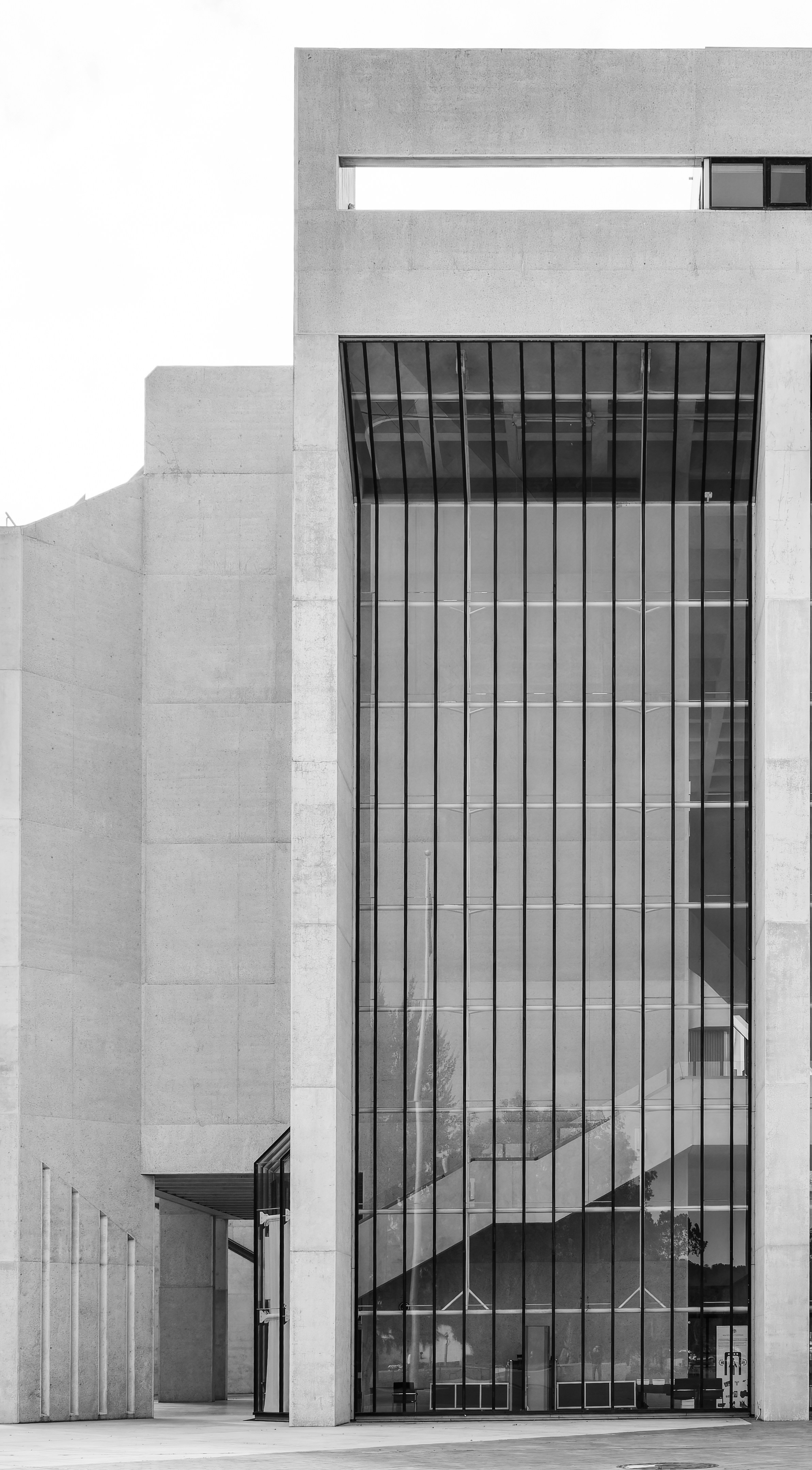 Monochrome photo of a modern concrete building with a tall, glass-front atrium and visible interior staircase, emphasizing geometric lines and minimalism.