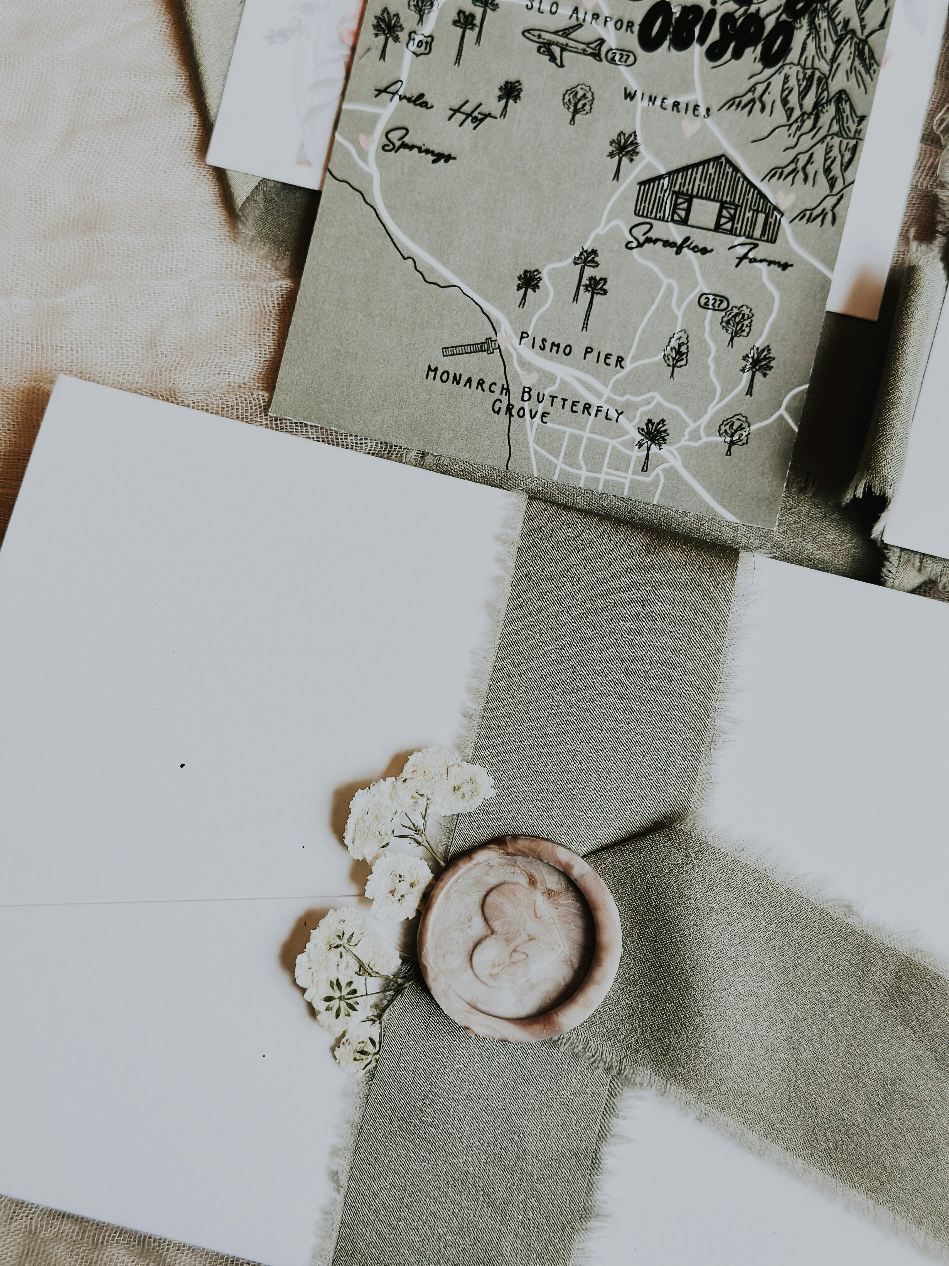 A white envelope with a wax seal and small white flowers on green ribbon