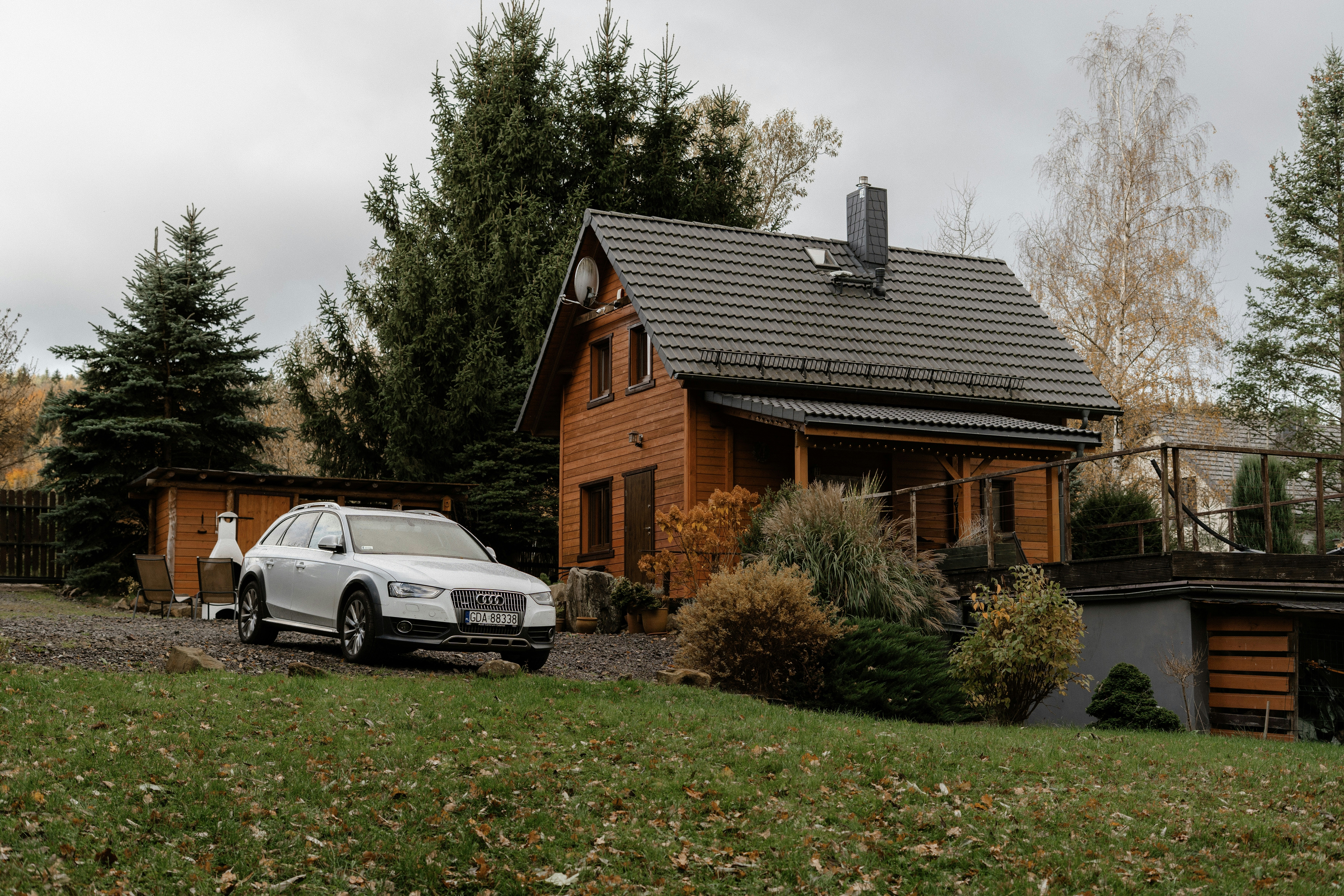 A white station wagon parked on a gravel driveway beside a wooden cabin
