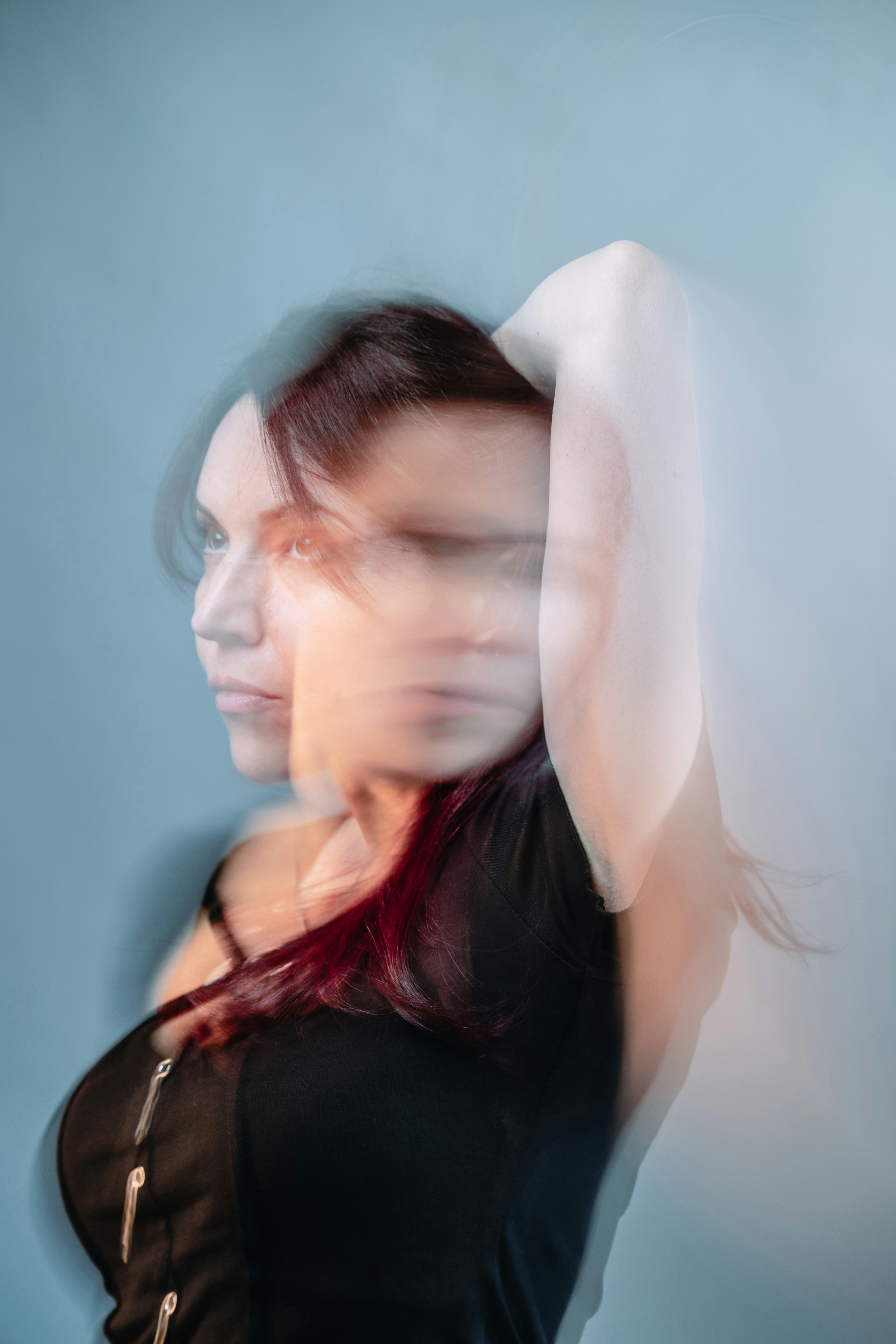 Soft blue studio backdrop with a multi-exposure portrait, showing a woman's face and upper body in motion blur against a dark top.