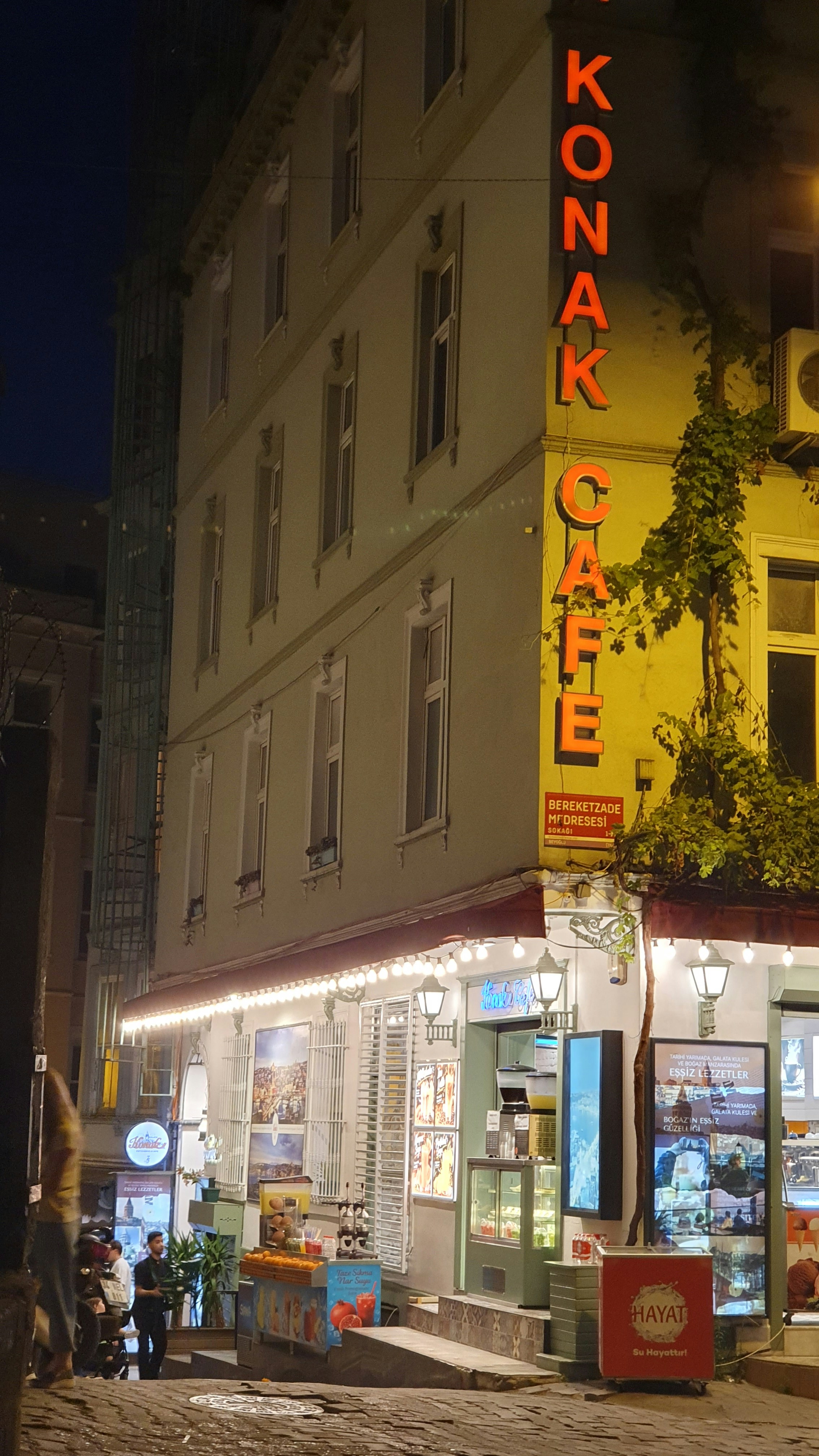 Neon Signage and Café Facade Along a Cobblestone Street