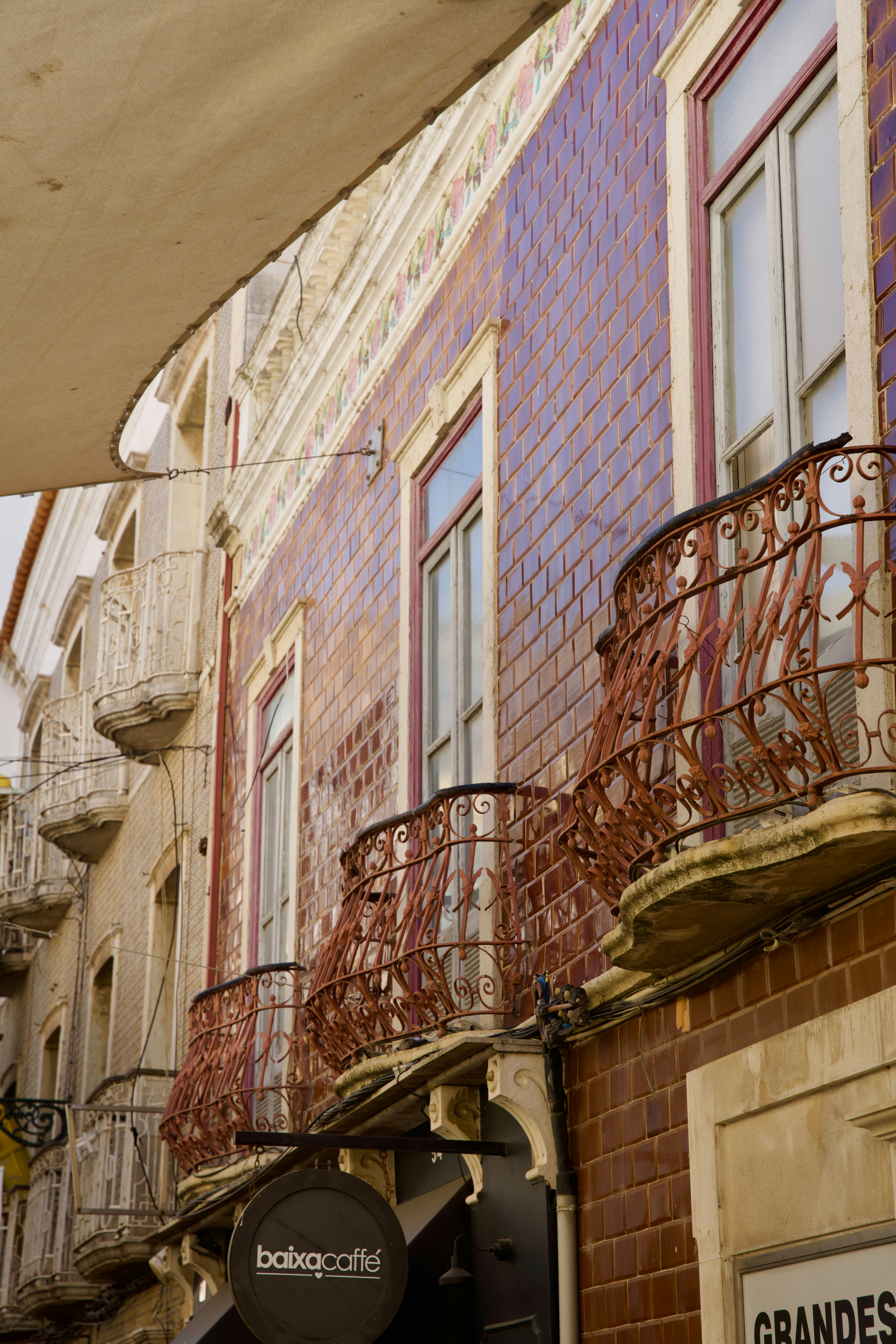 Colorful tiled building façade with ornate wrought-iron balconies and a small café sign, captured in warm afternoon light.
