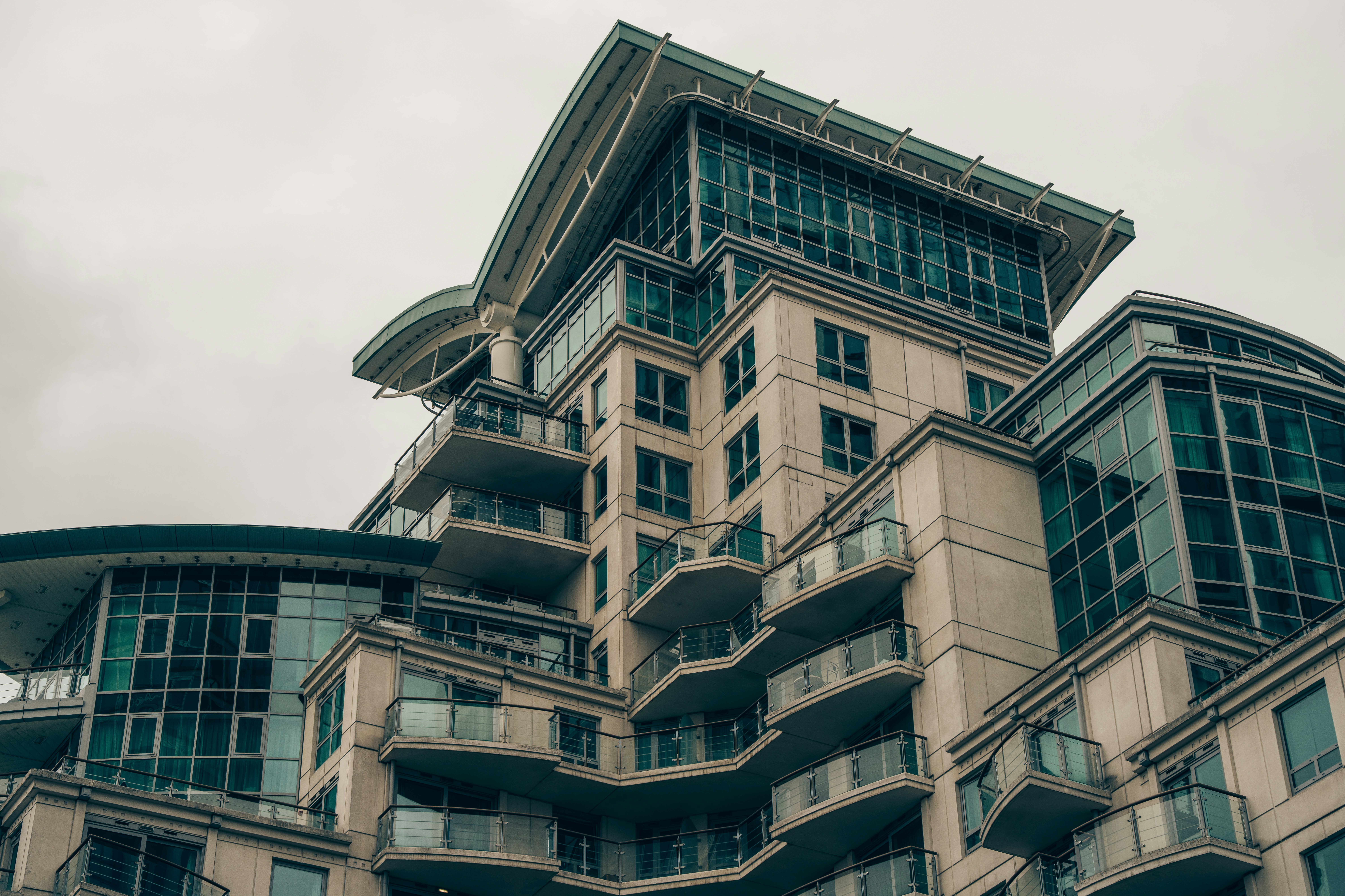 Architectural detail of a multi-wing apartment building with glass balconies and stepped setbacks, emphasizing geometric forms and the overcast sky.