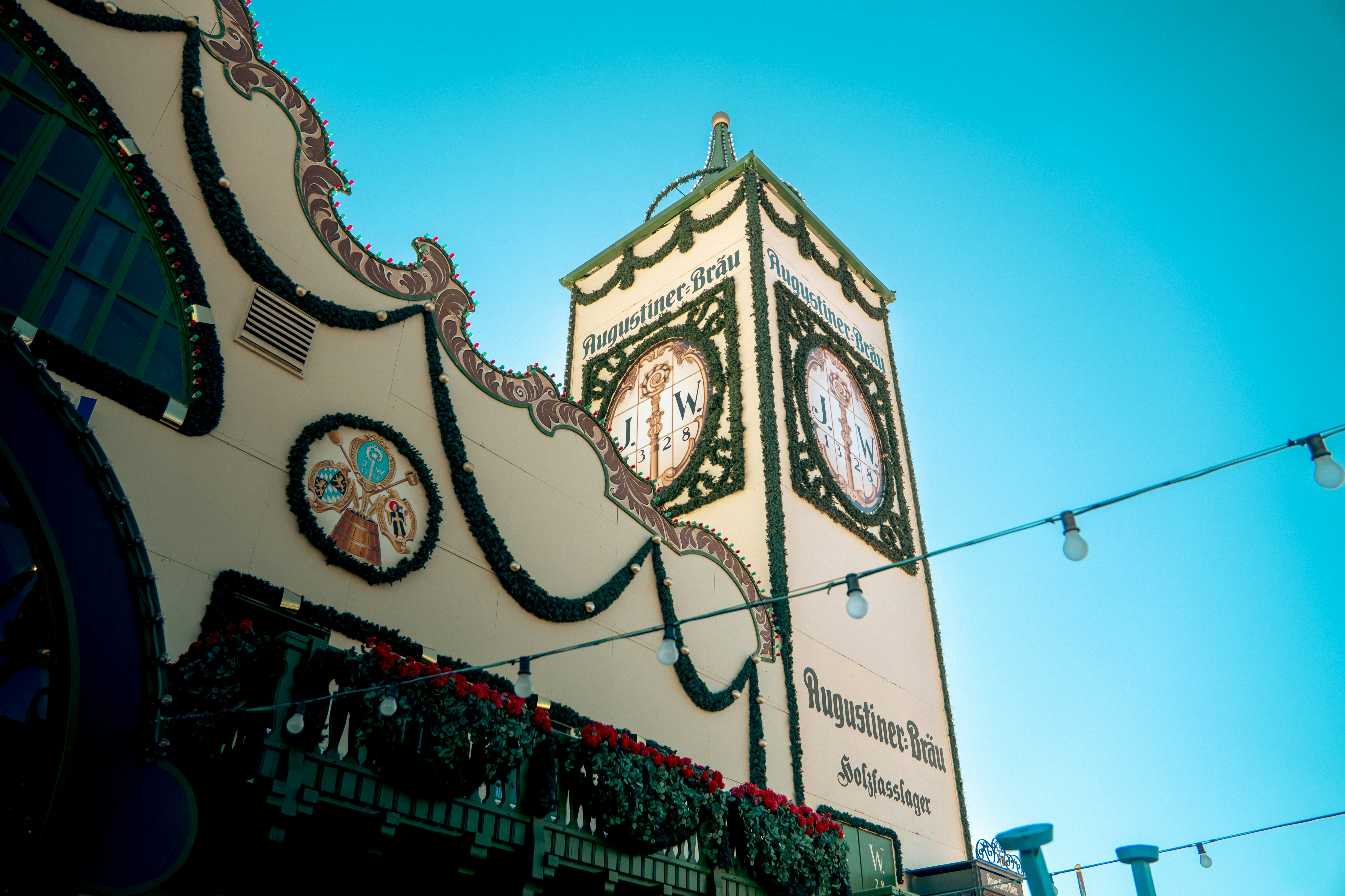 Colorful European-styled building with a prominent clock tower, string lights, and decorative facade; a lively street scene highlighting architecture and festive atmosphere.
