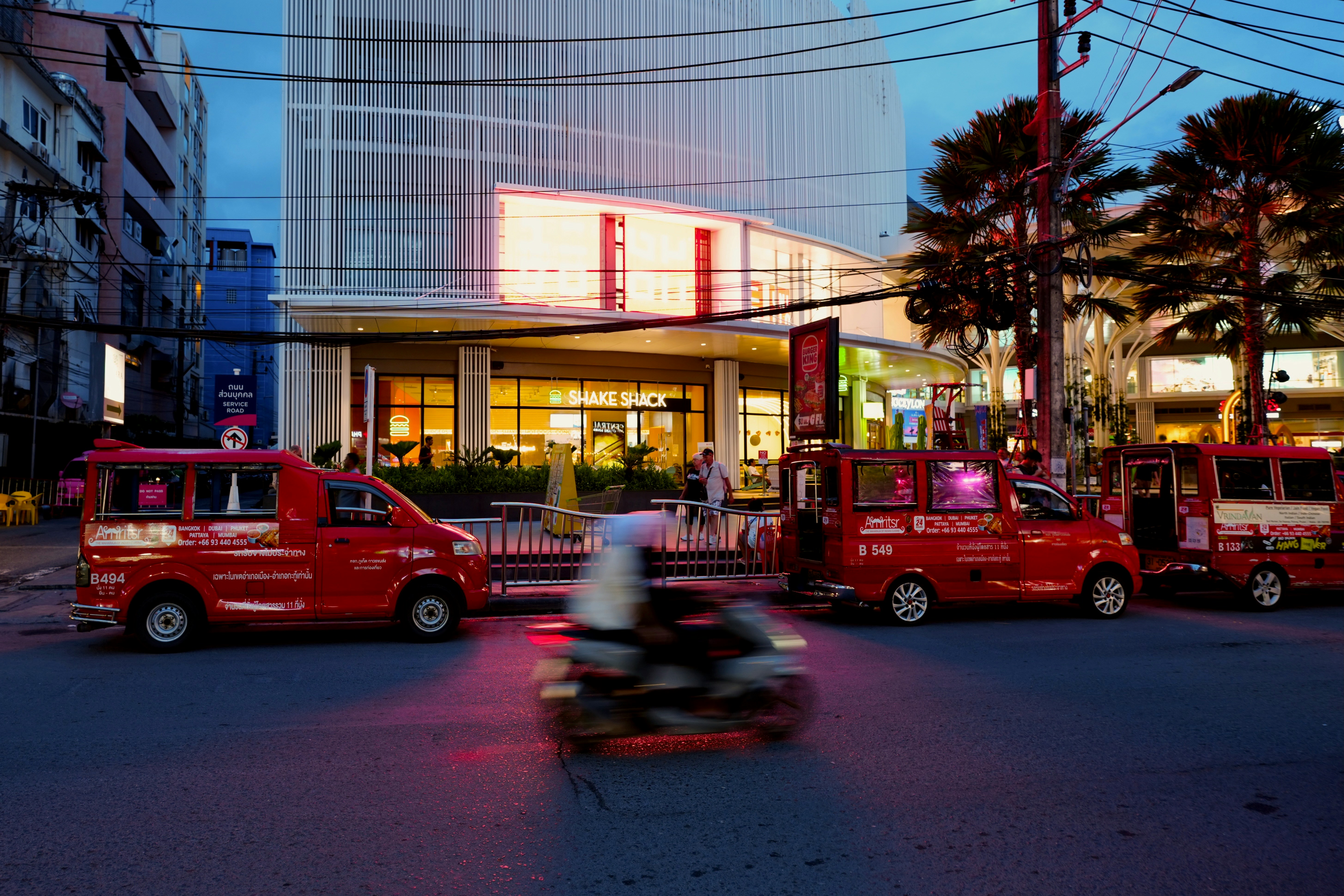 Colorful yellow songthaew taxis parked on a bustling street corner near Central Patong at dusk.