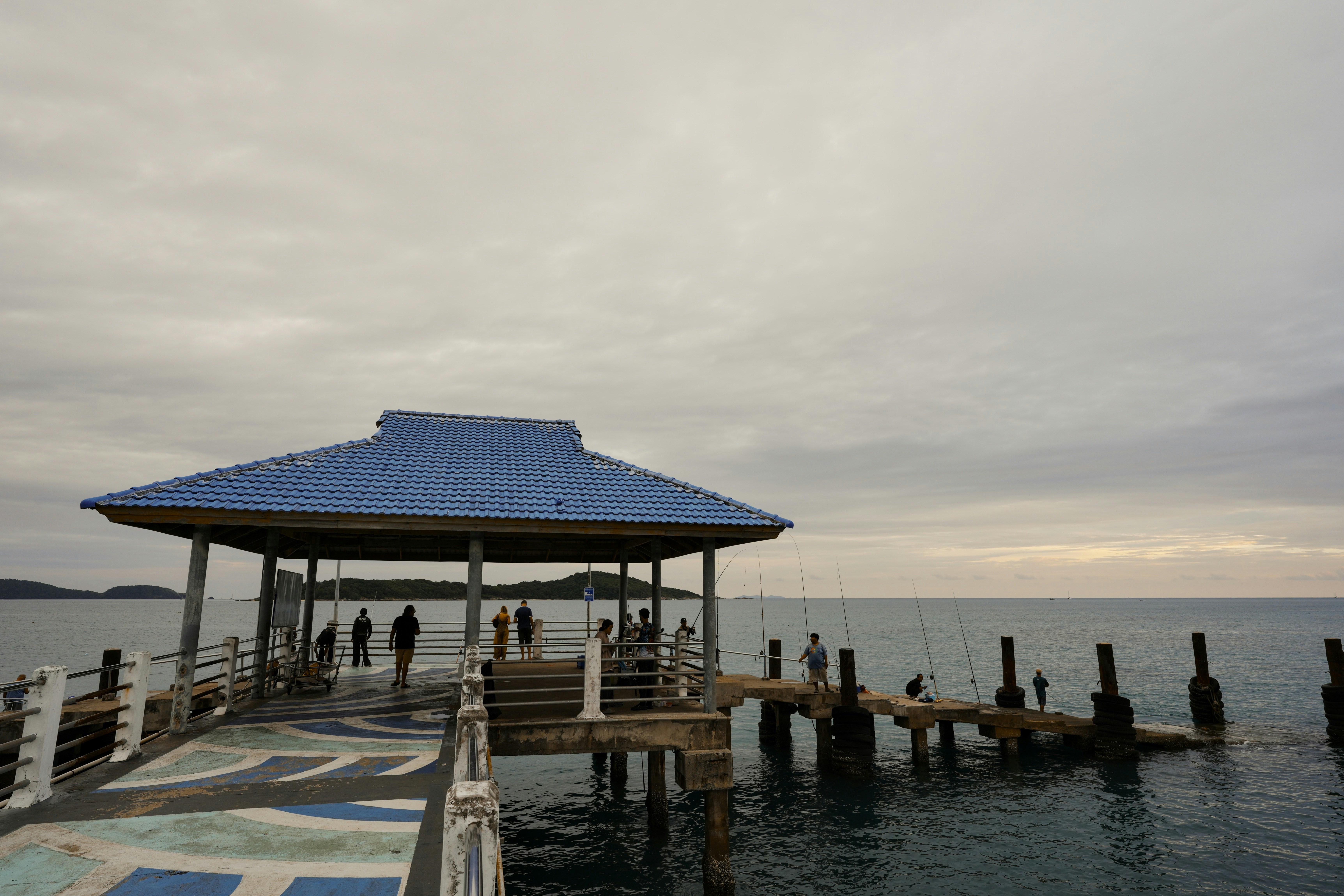Pier Pavilion at Dusk: People, Water, and a Blue-Tiled Roof