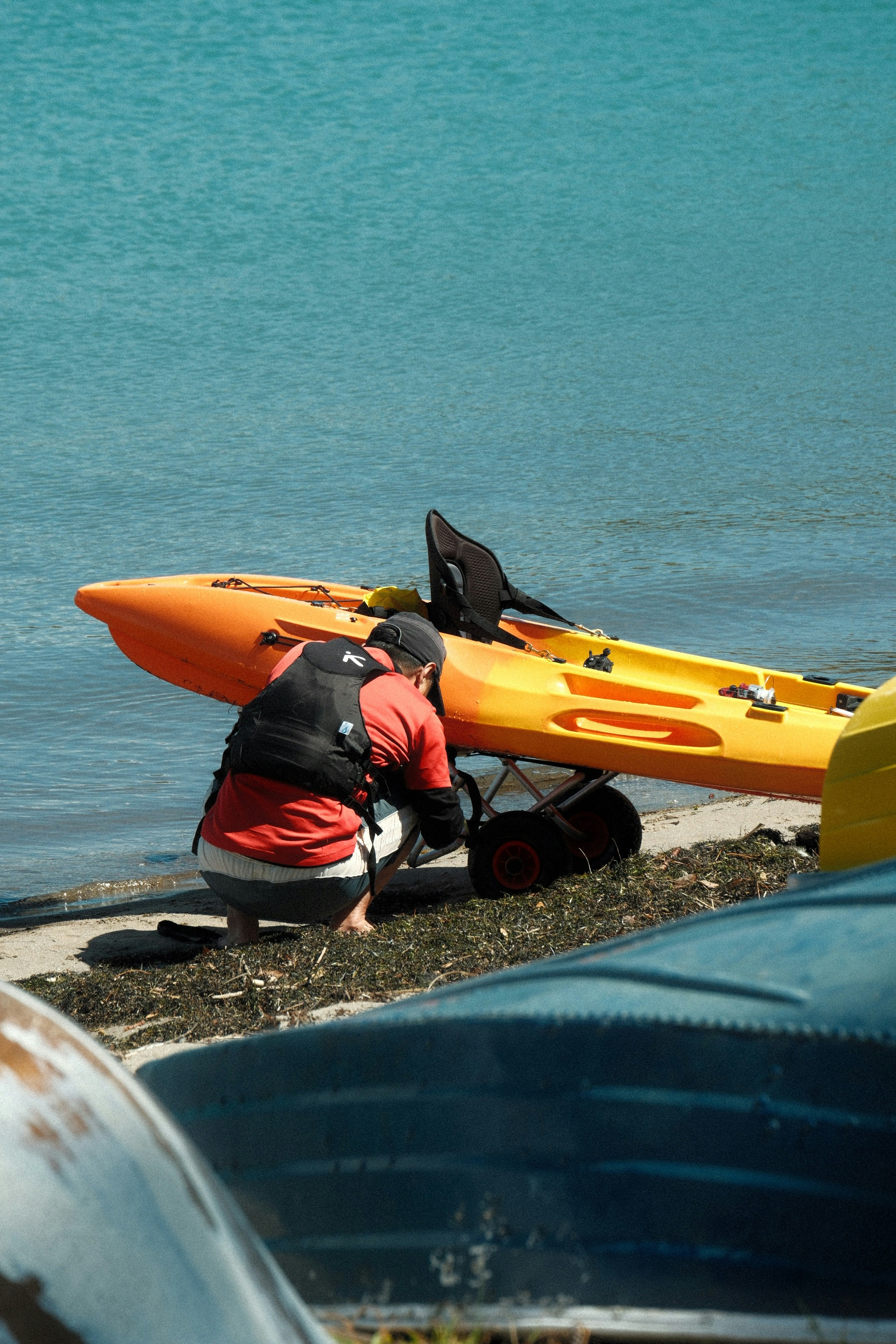 Crew member servicing a bright orange kayak beside a calm shoreline