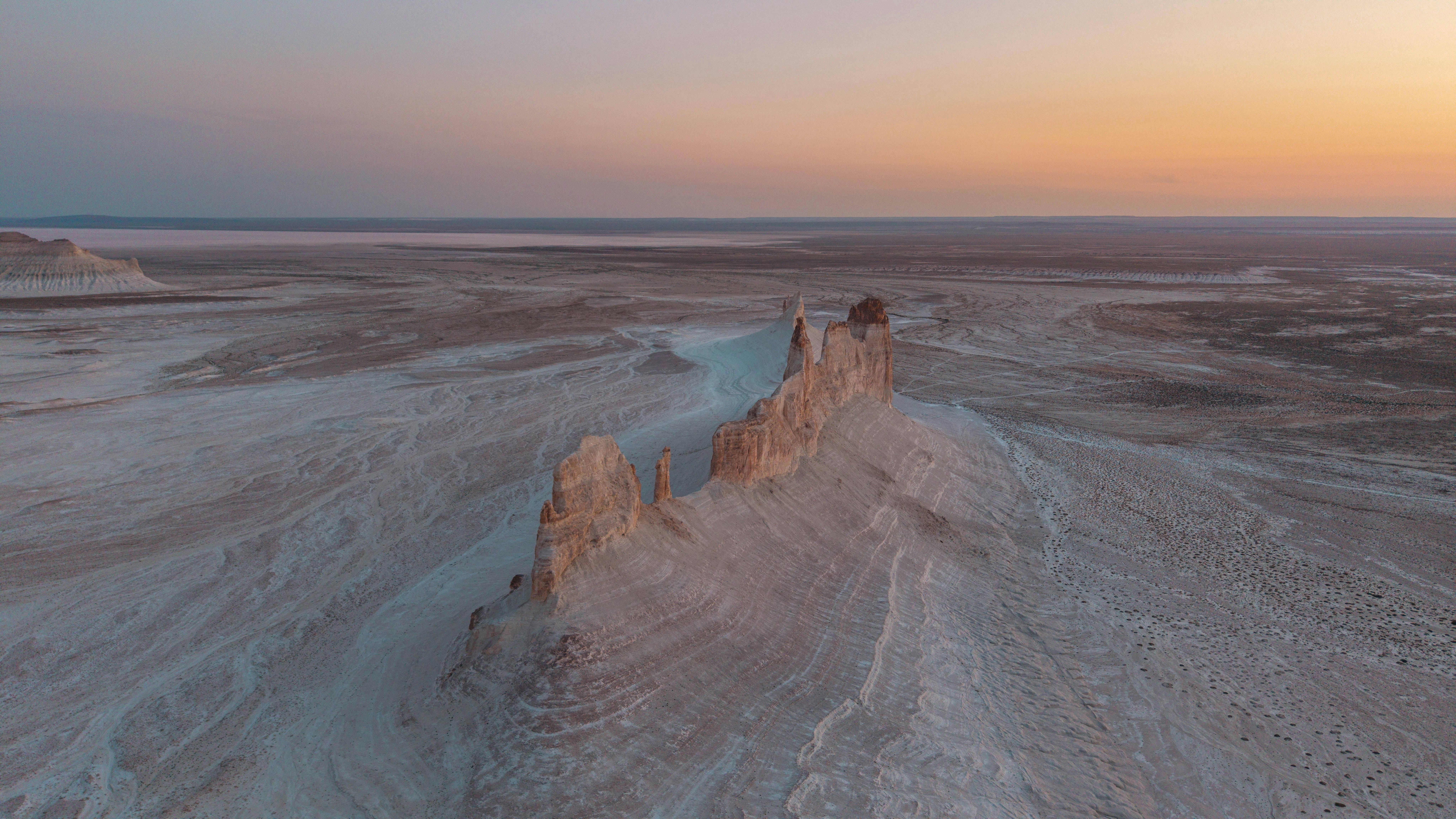 Eerie desert plateau with eroded rock spires under a pale sunset, capturing the expansive shoreline-like plain and weathered formations.