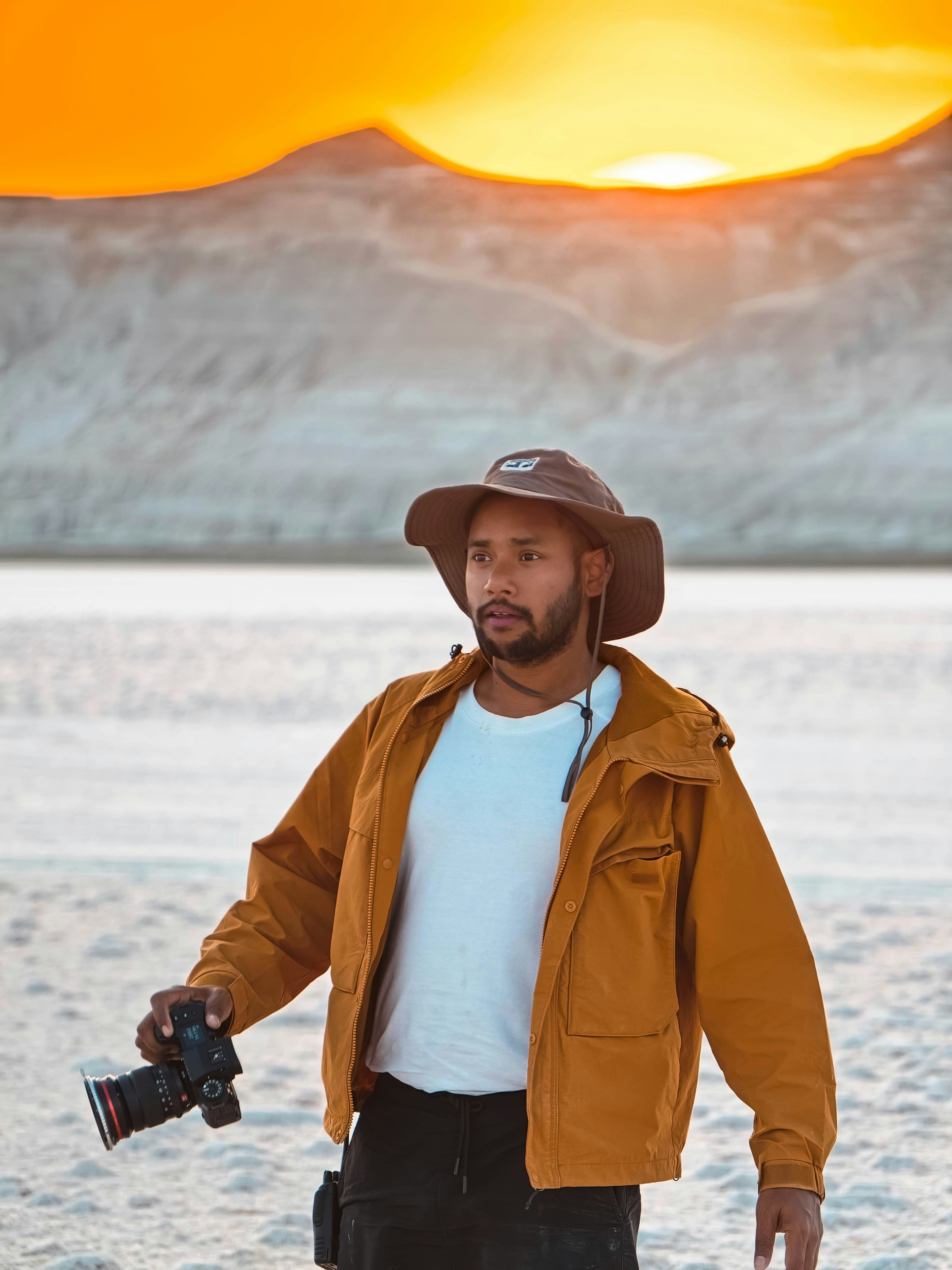 A man in a brown hat and jacket holding a camera against a bright sky