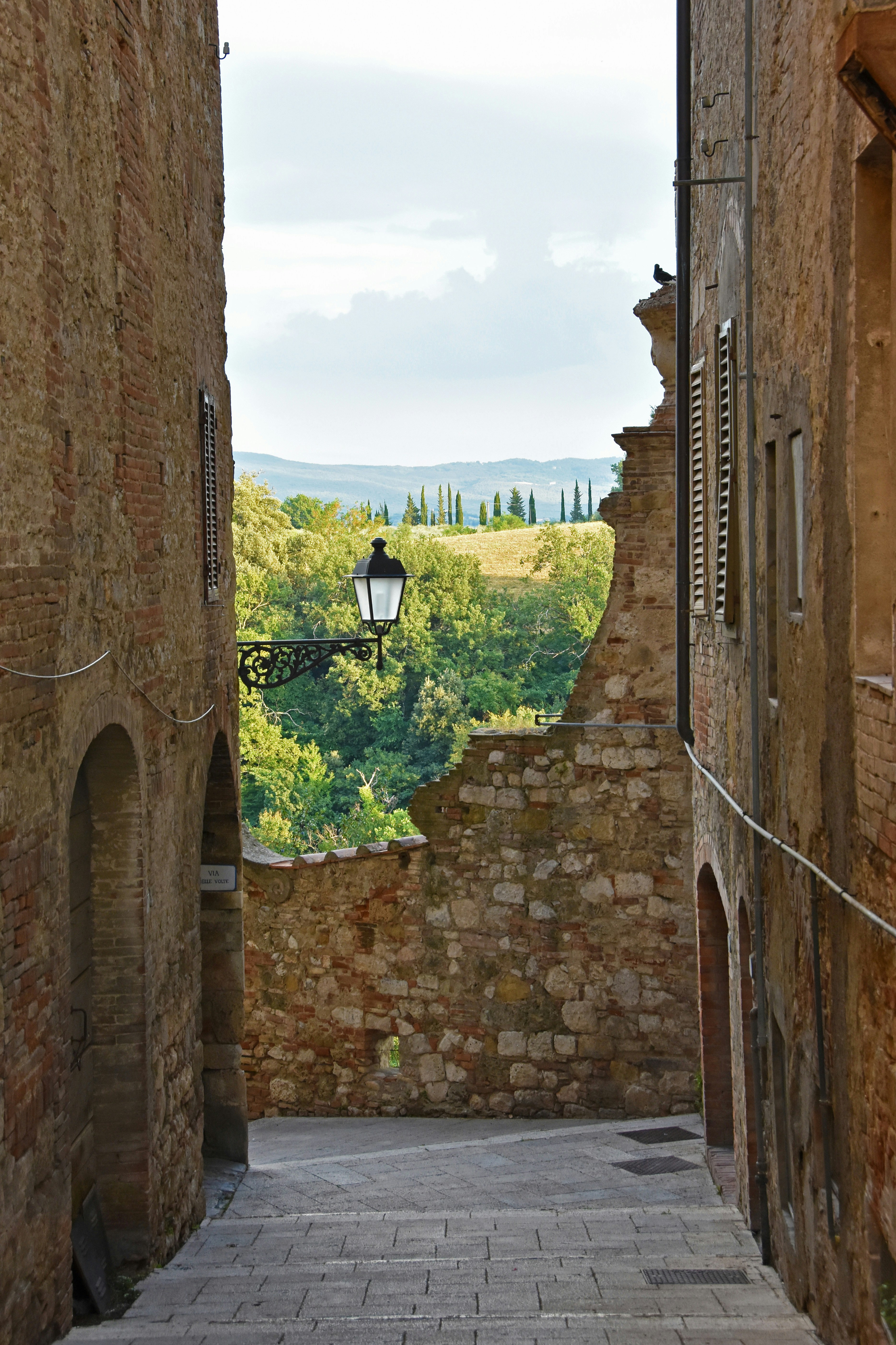 Sunlit Canal Between Ancient Walls: A Pedestrian Path Framing Tuscan Hills