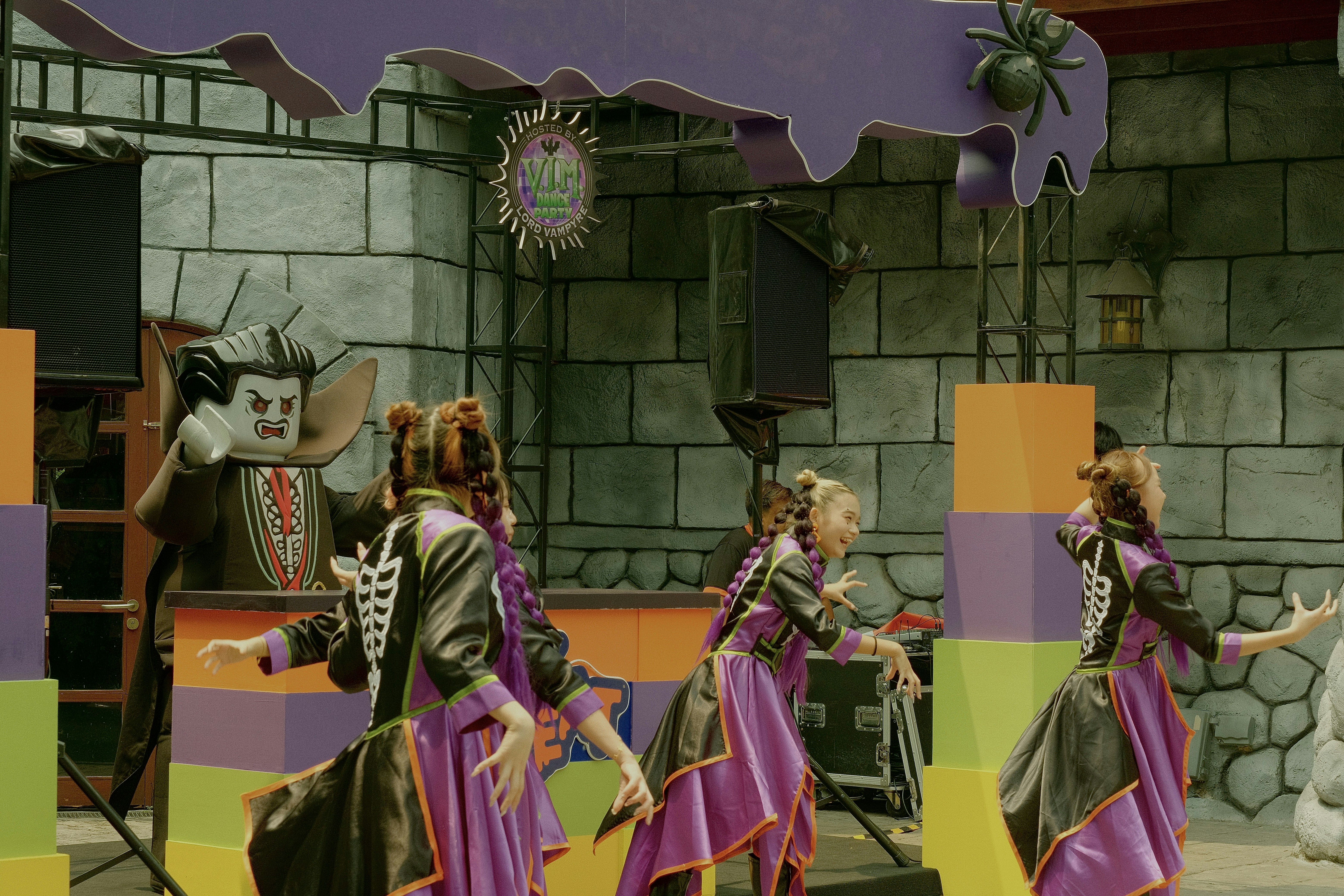 Masked Stage Stroll: Dancers in Violet and Black on a Colorful Platform