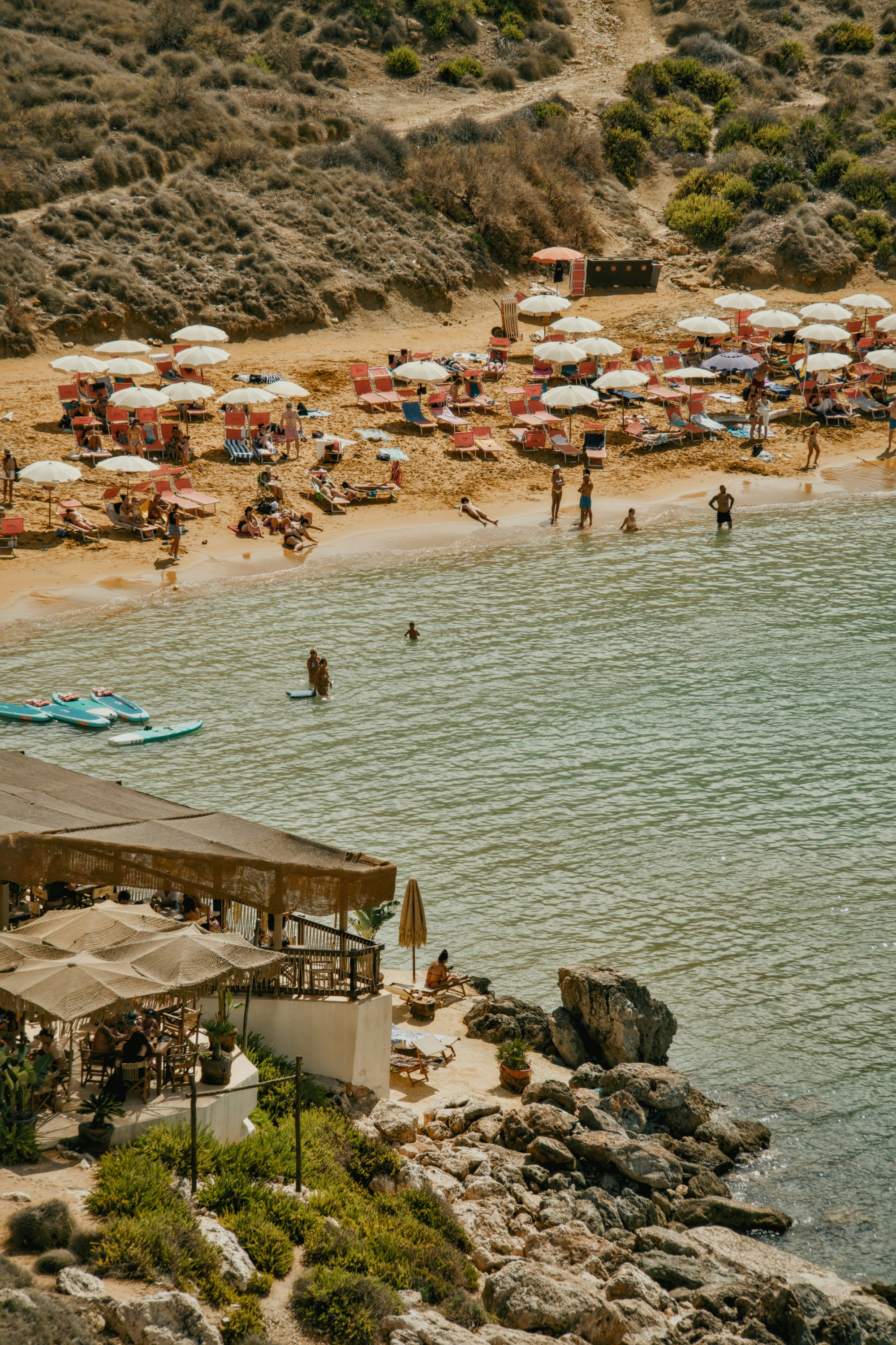 Sunlit Beachside Oasis: Umbrellas, Turquoise Shore, and Cliffside Café