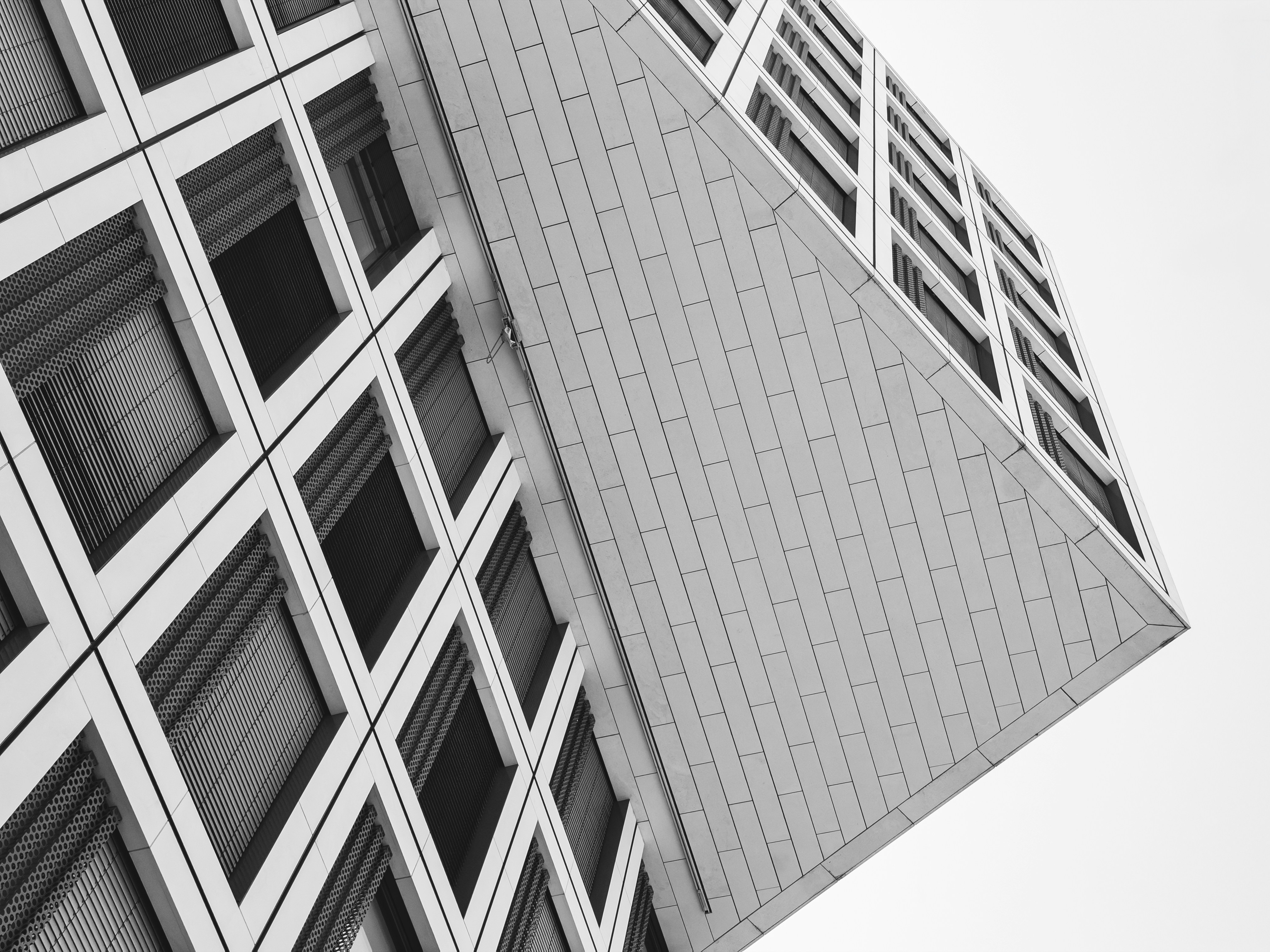 Geometric facade of a modern building with angular perspective and grid windows in grayscale; emphasizes architectural pattern and depth.