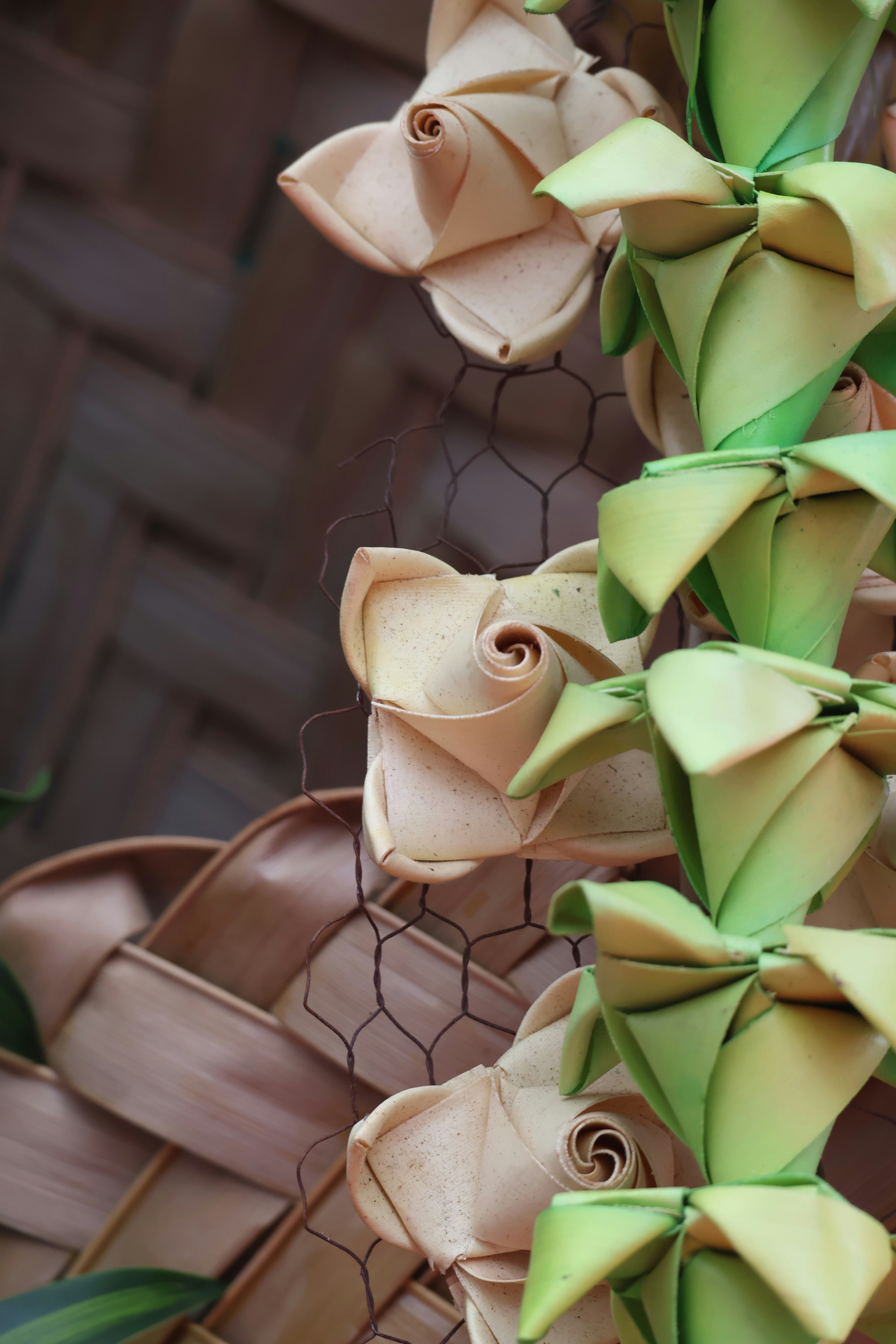 Close-up of a vertical arrangement of woven paper rosettes in beige and green, linked along chicken wire for a decorative garland.