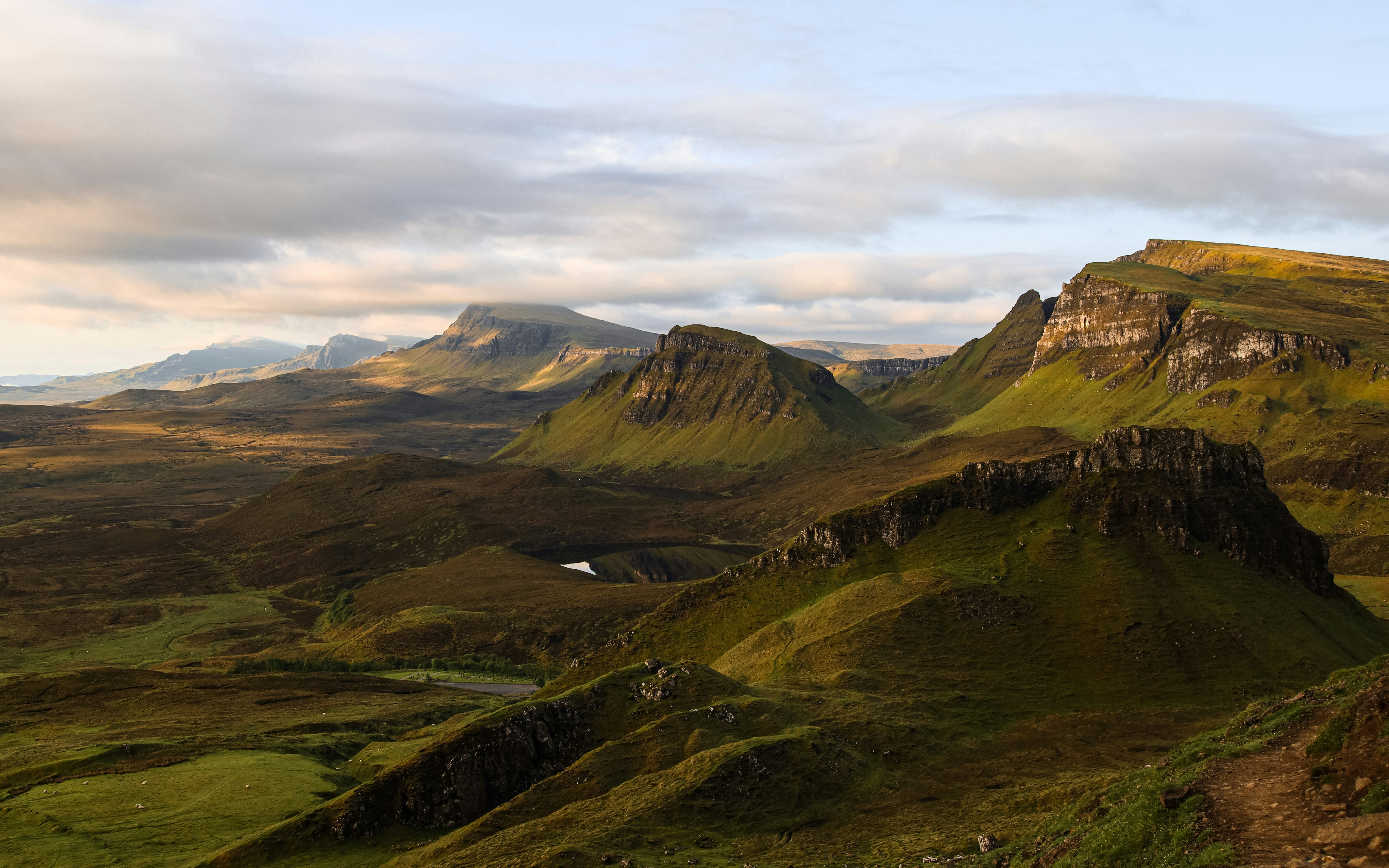 Horizon panorama of rolling green hills and rugged ridge under a partly cloudy sky, with distant mountains fading into the background.