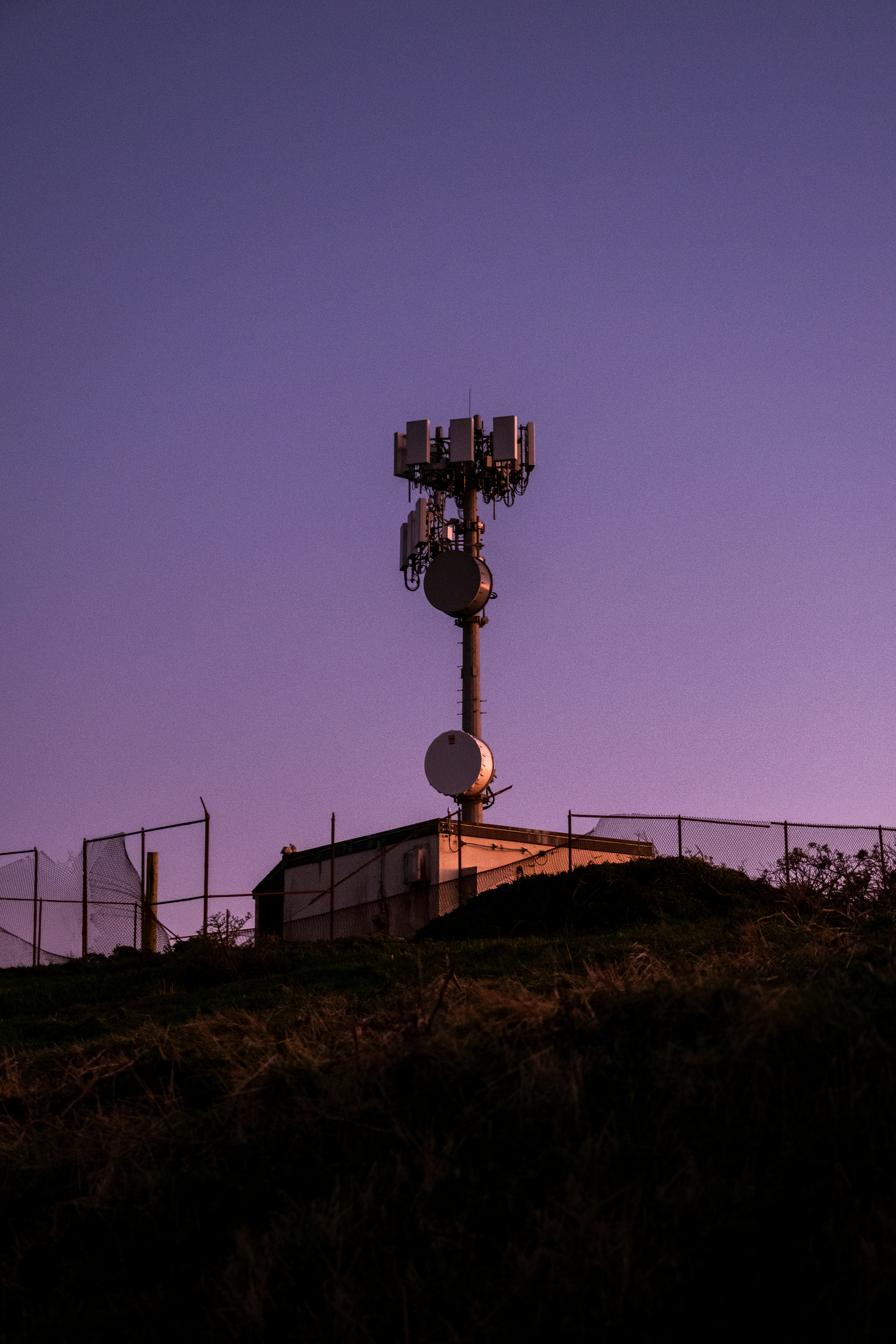 Cell Tower Silhouette at Dusk on a Fenced Hill