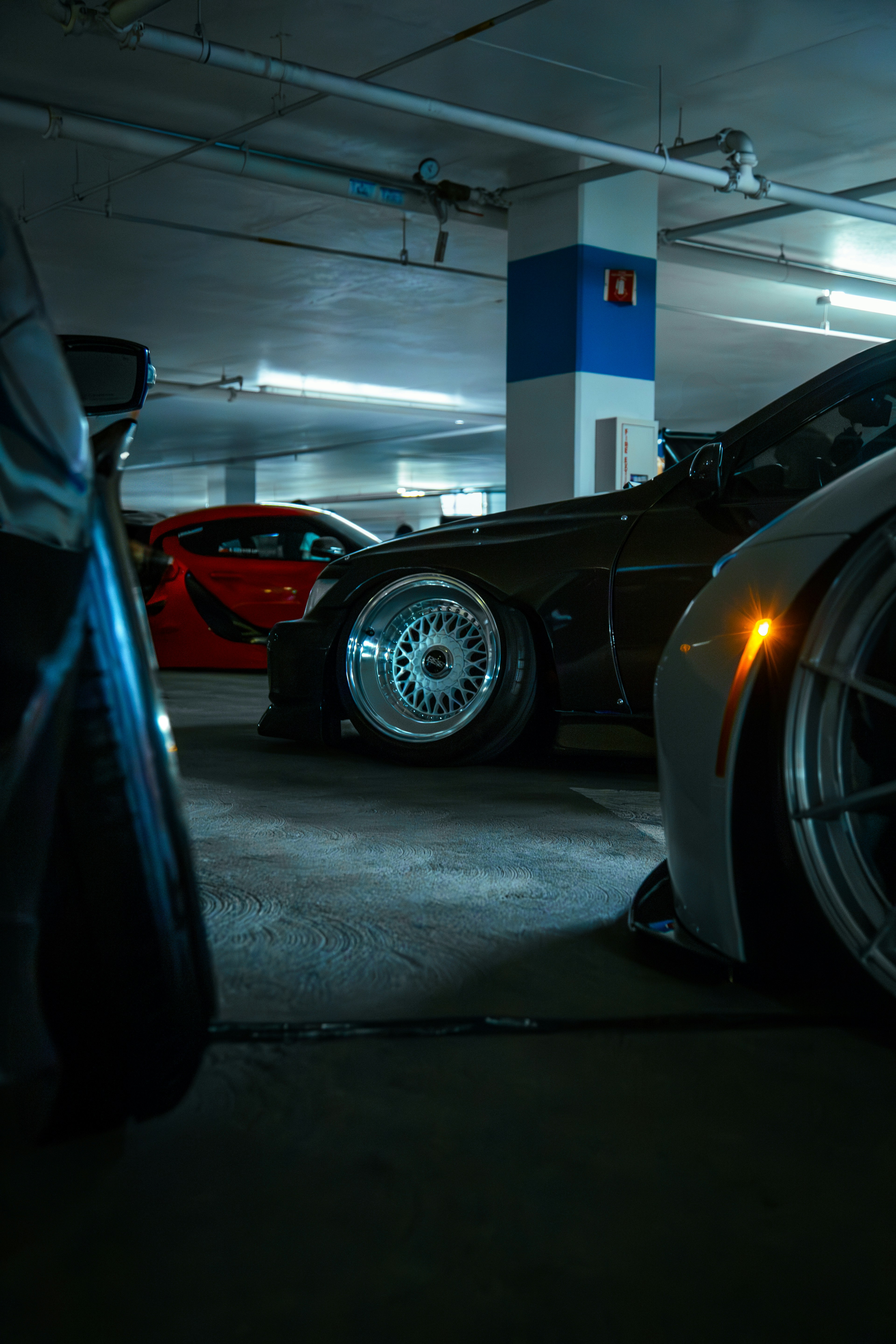 Low-Angle Night in a Locked Parking: A Sleek Matte-Black Porsche and a Glowing Wheel