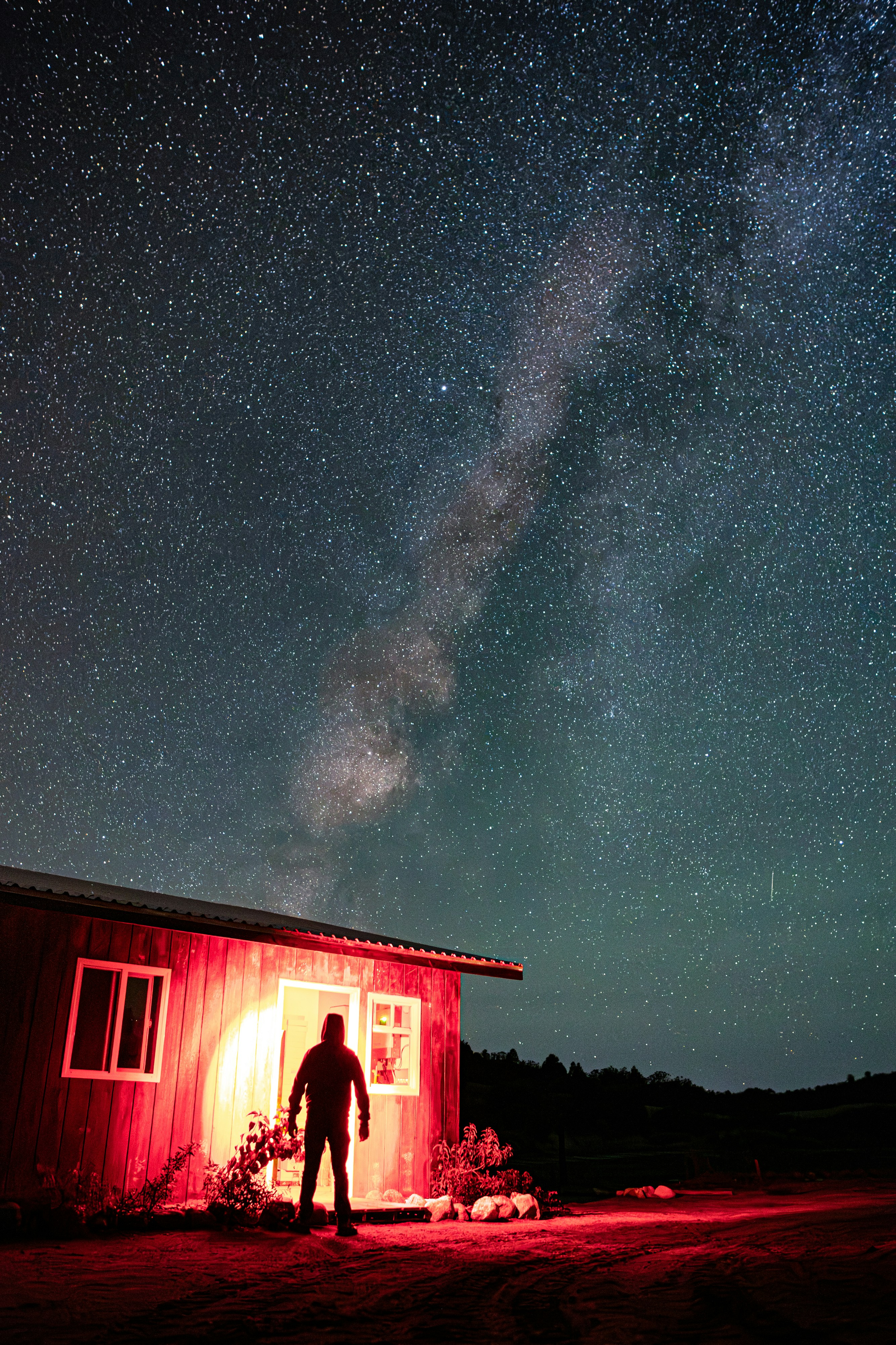 Milky Way Patrol: A solitary figure under a red-lit cabin and a sky full of stars