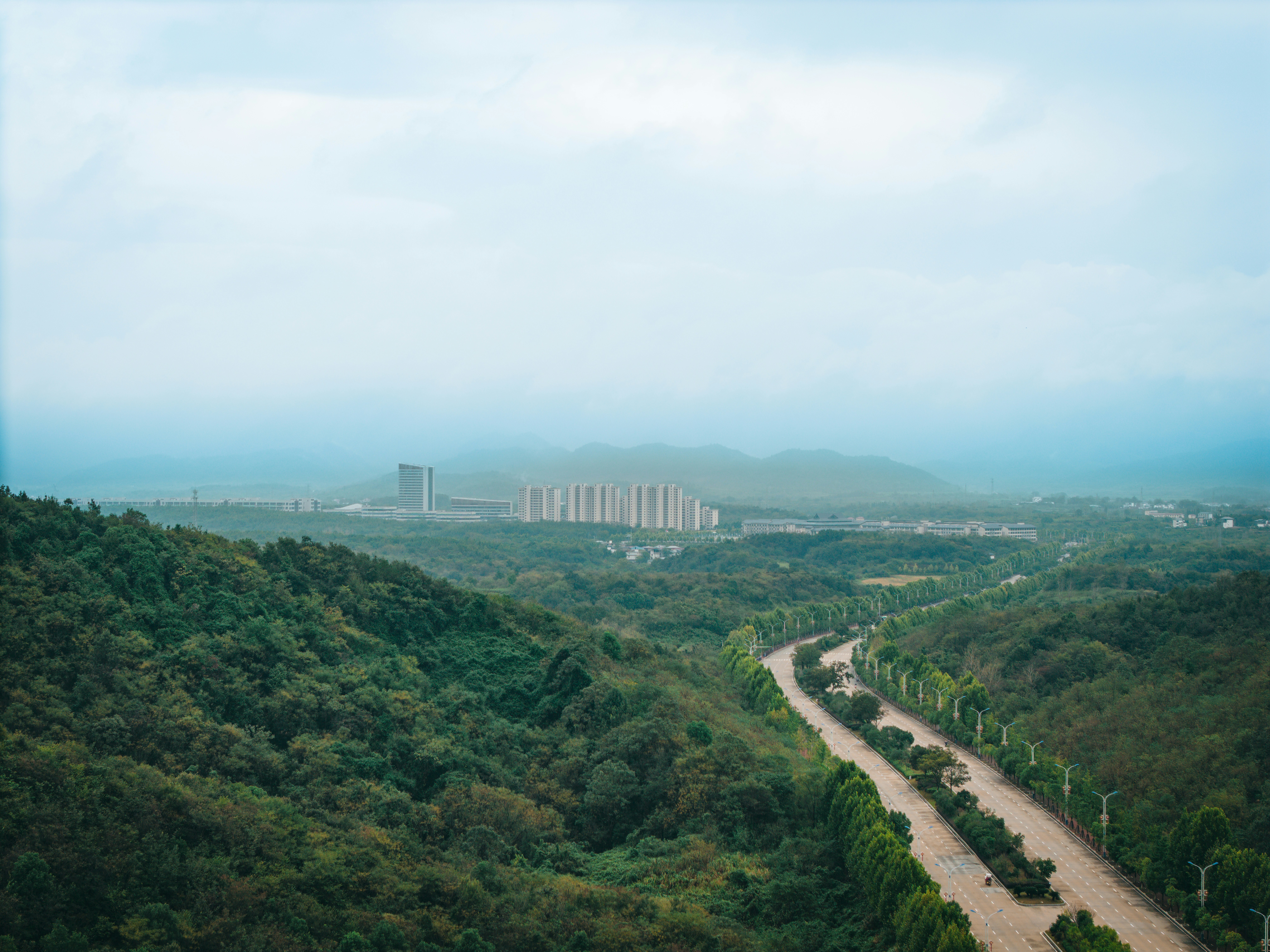 Ribbon Road Through Verdant Hills with Distant Urban Silhouette