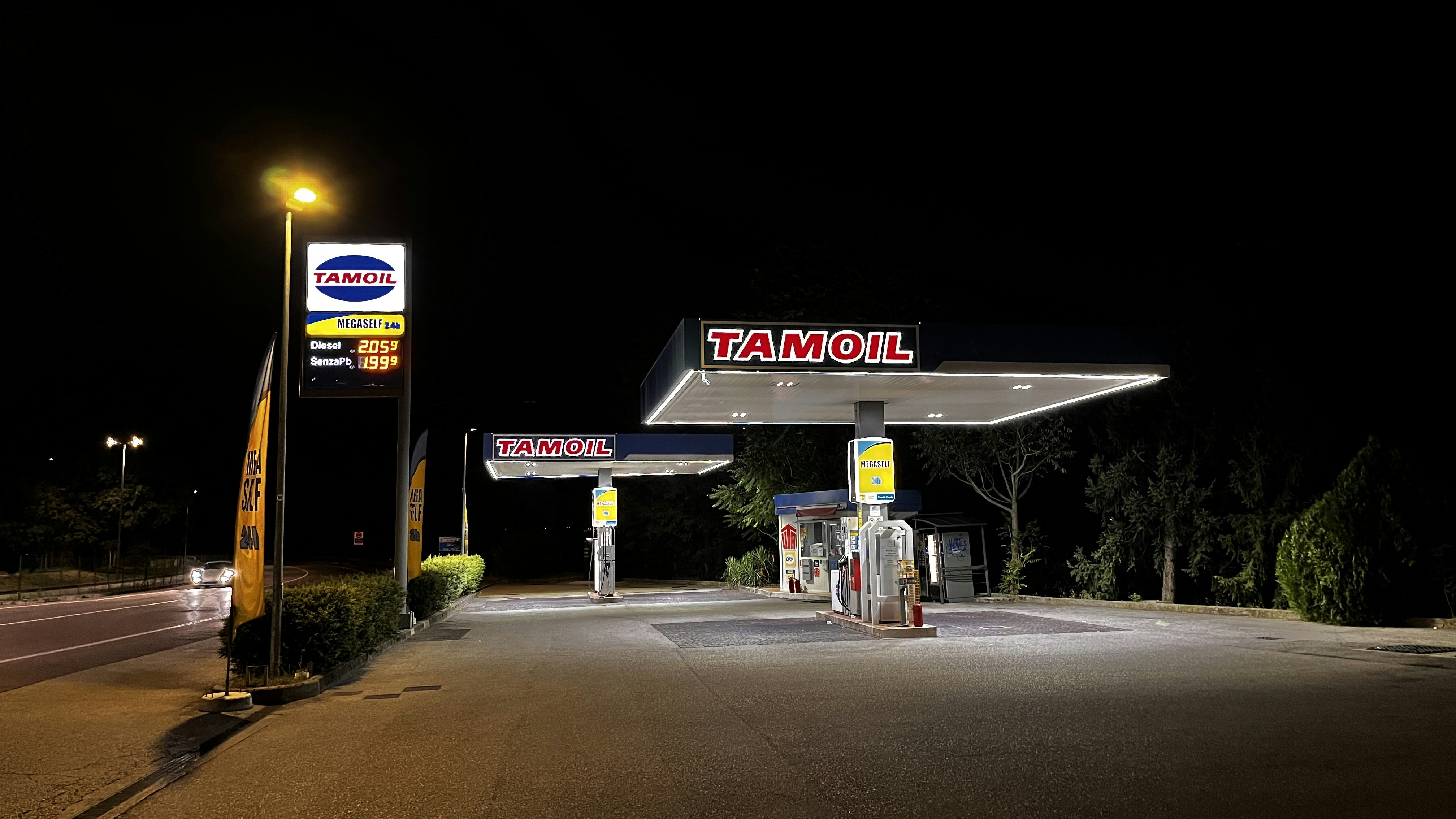 A quiet Bitcoin-lit gas station rests under a dark sky, with bright canopies and empty forecourts, illuminated signage casting reflections on the pavement.