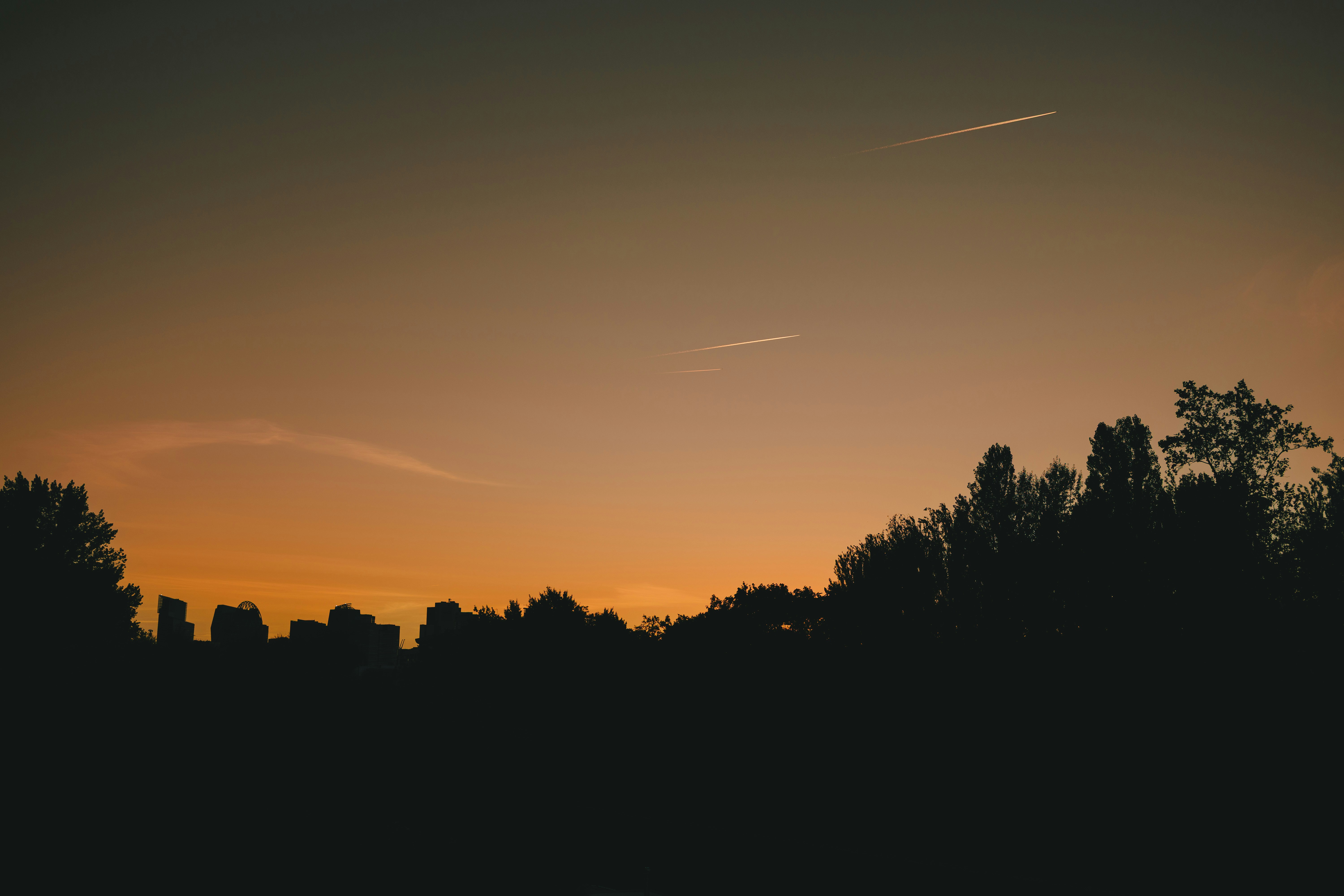 Sunset Silhouette Over City Edge with Contrails