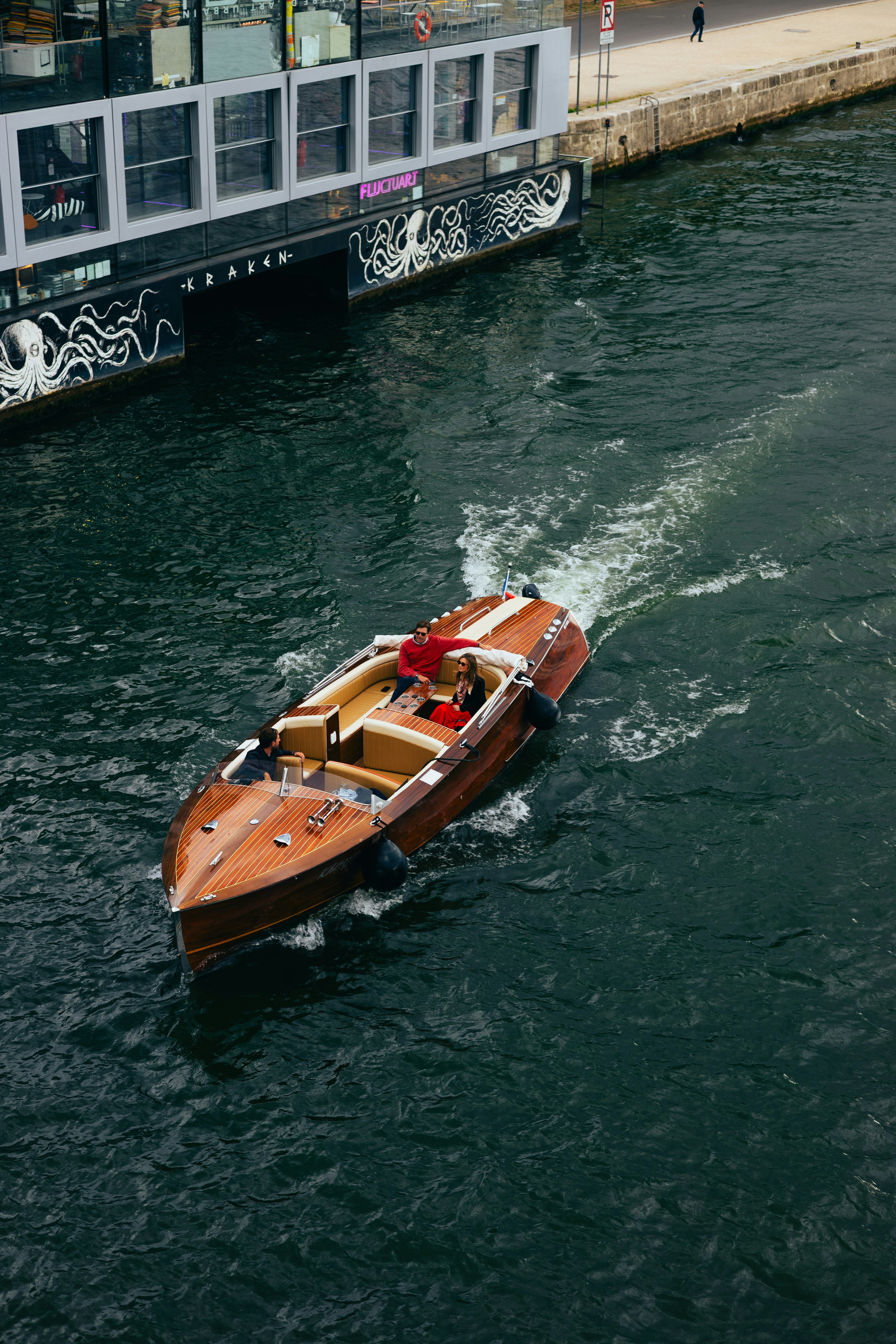 Wooden speedboat carving a wake past a dockside mural