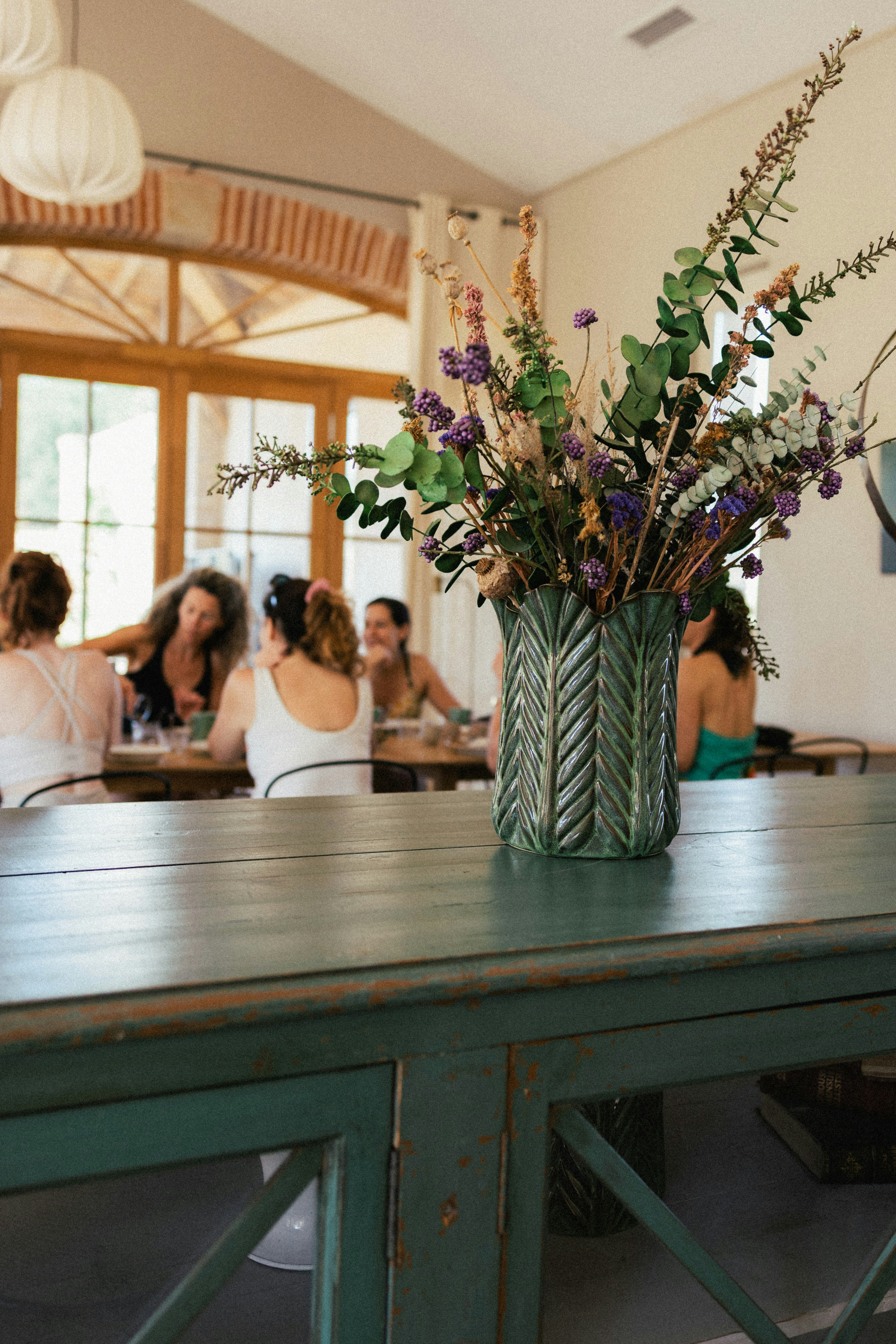 Floral centerpiece in a sunlit gathering room framed by blurred guests