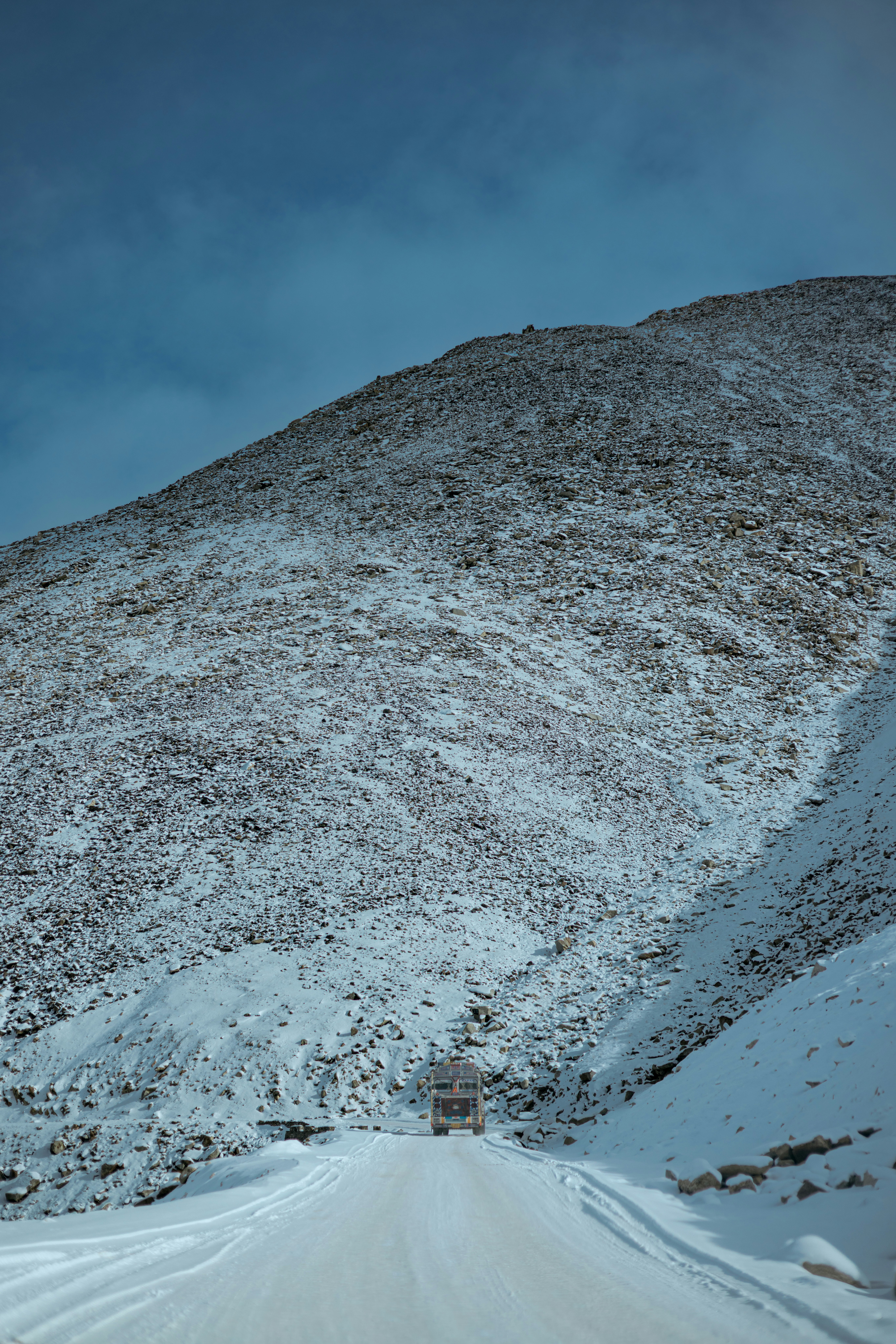 Snowbound Pass: A Lone Truck Traverses the Slopes Beneath a Blue Skied Rim